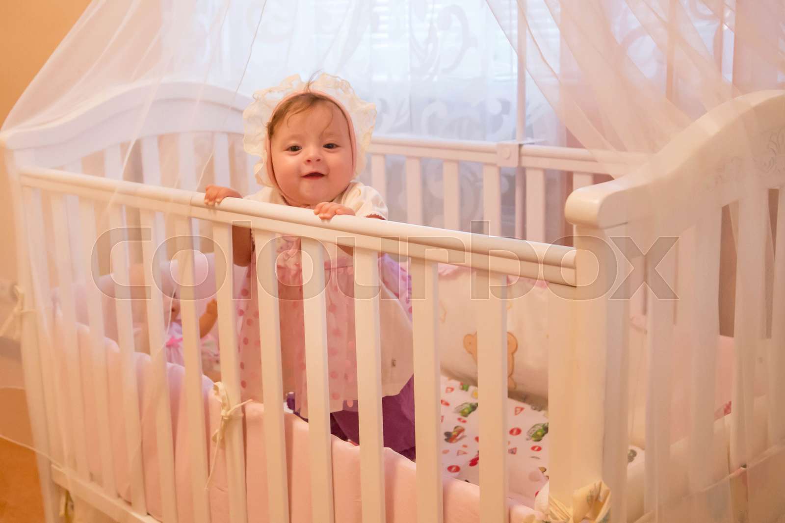 Baby girl standing in her crib. | Stock image | Colourbox