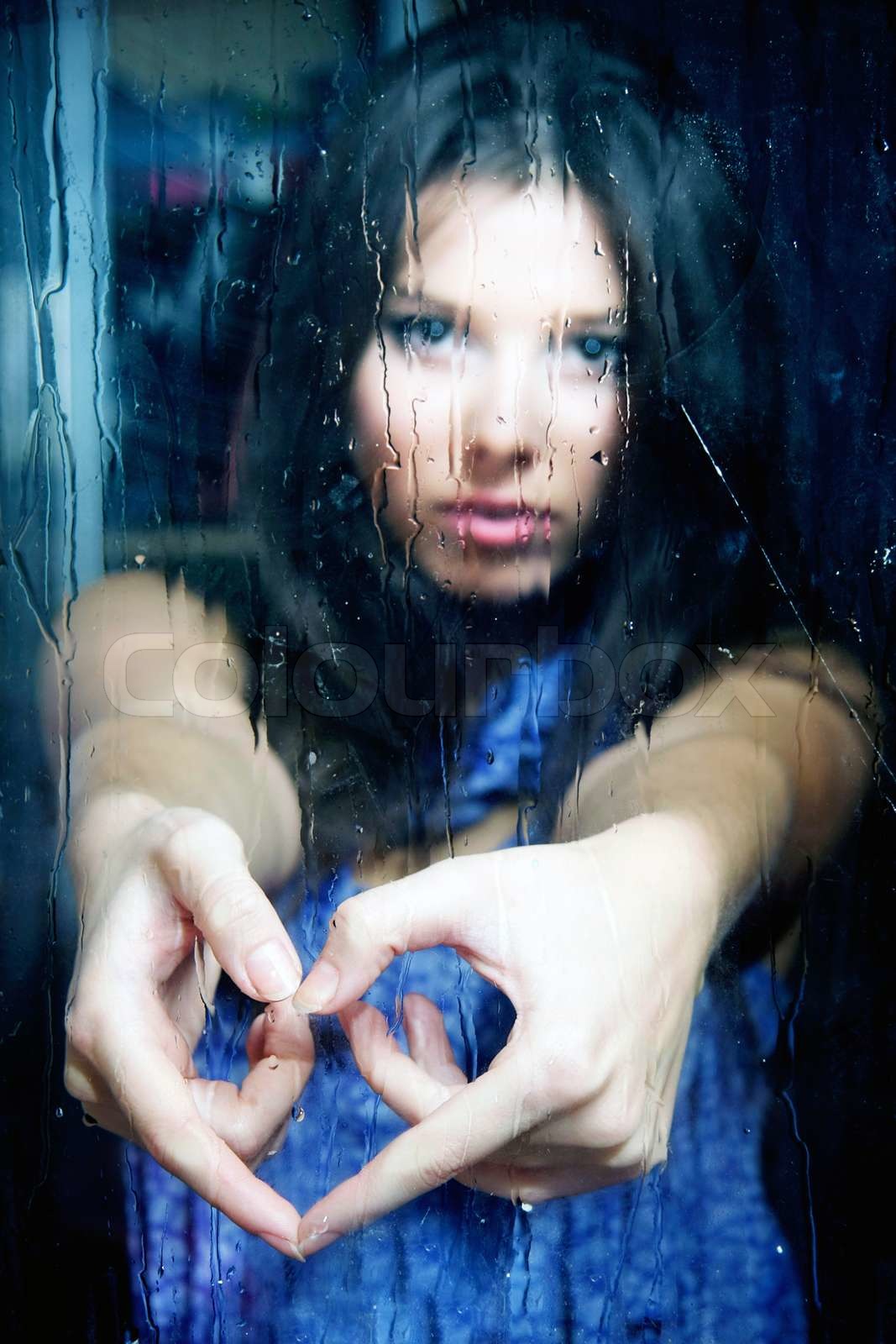 young girl making heart from fingers behind wet window | Stock image ...