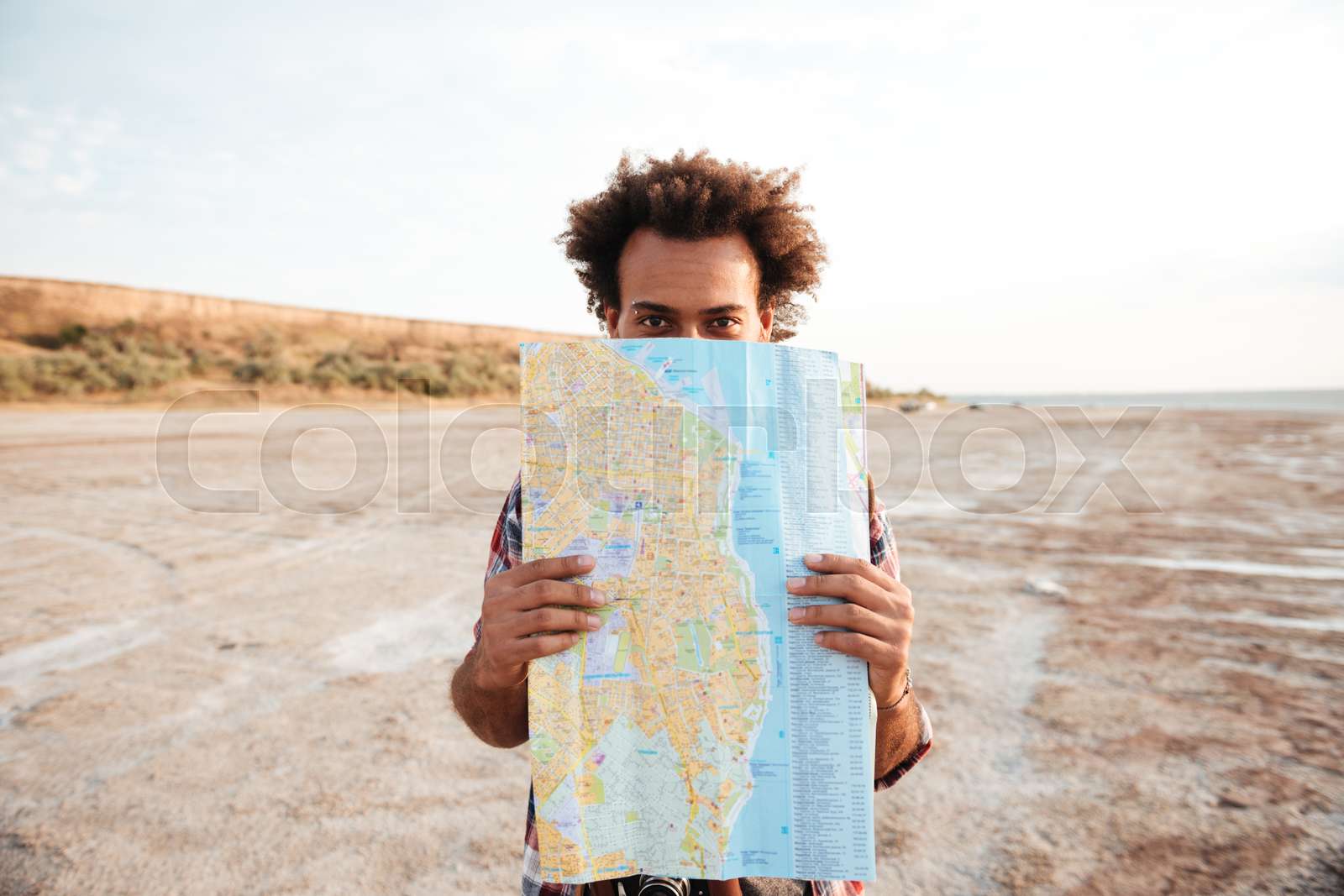 Playful man standing and hiding behind map outdoors | Stock image ...