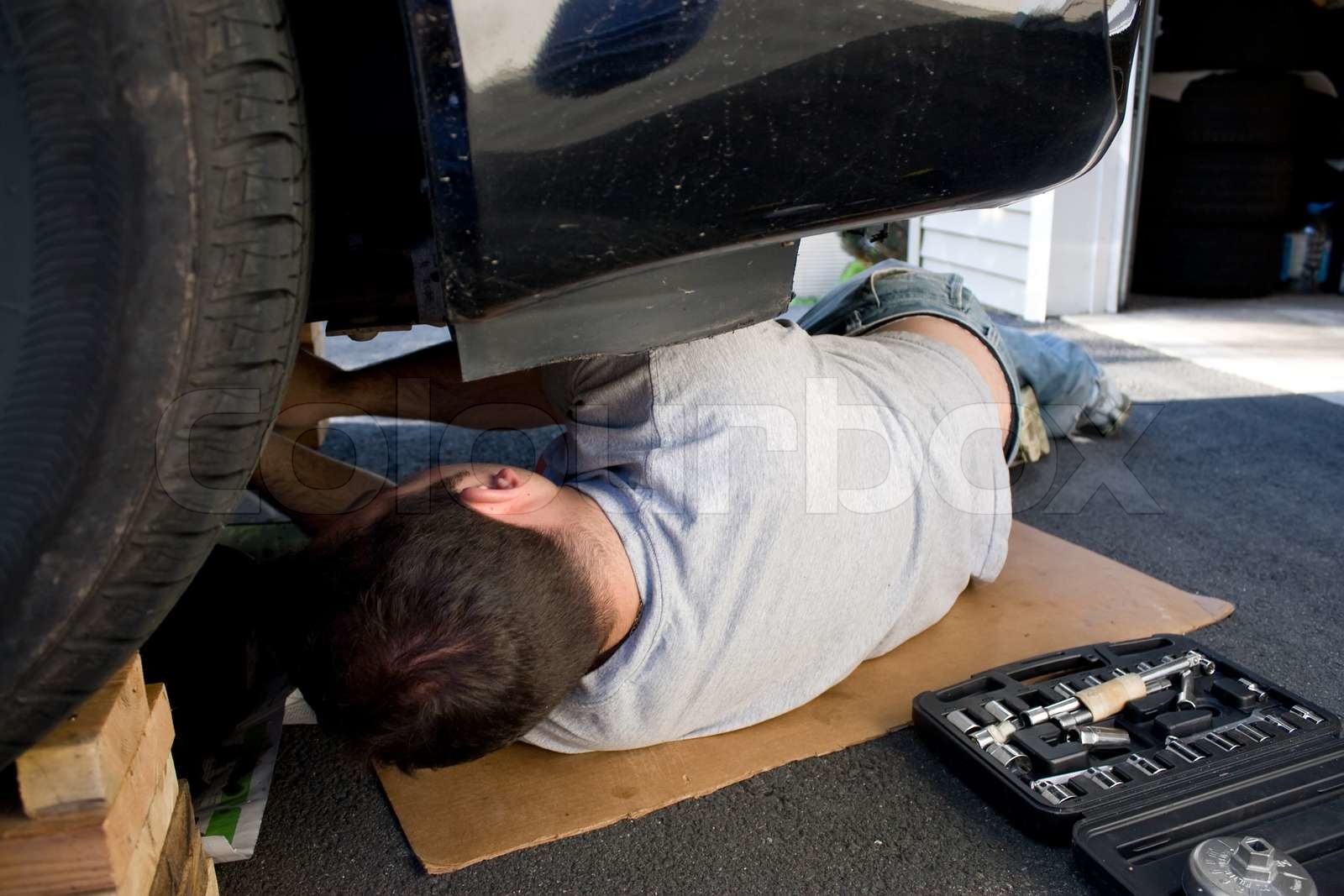 A young man laying underneath a car doing repairs or maintenance on the ...
