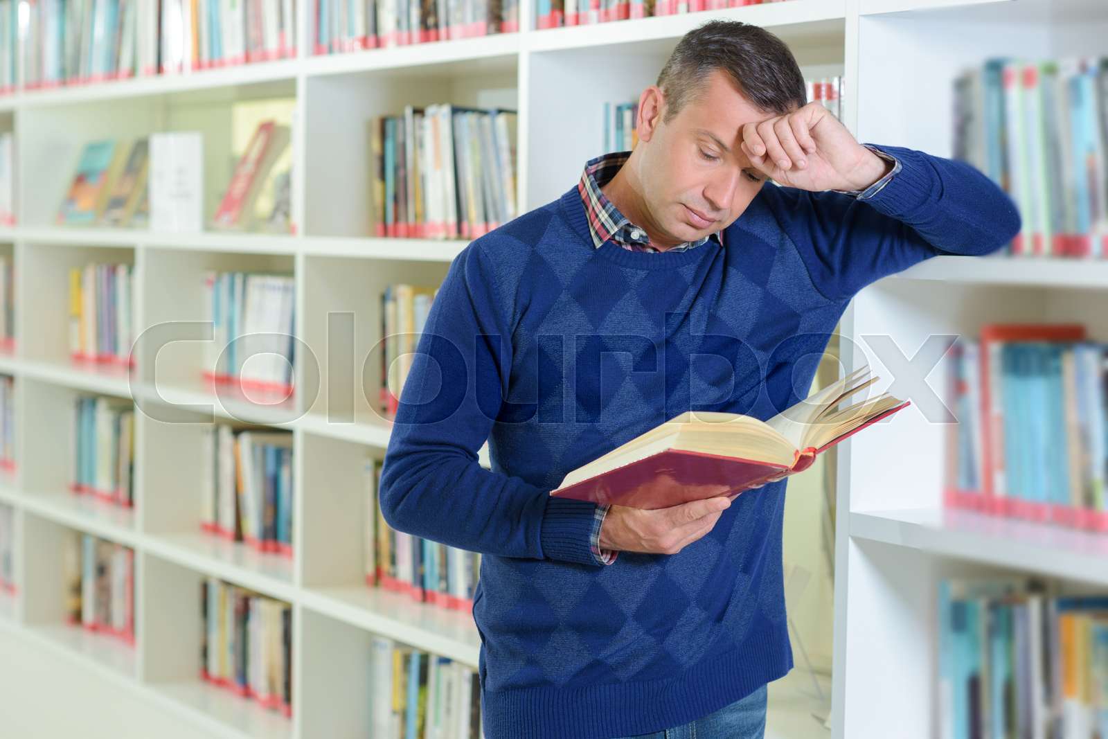 Man reading in library, resting head on hand | Stock image | Colourbox