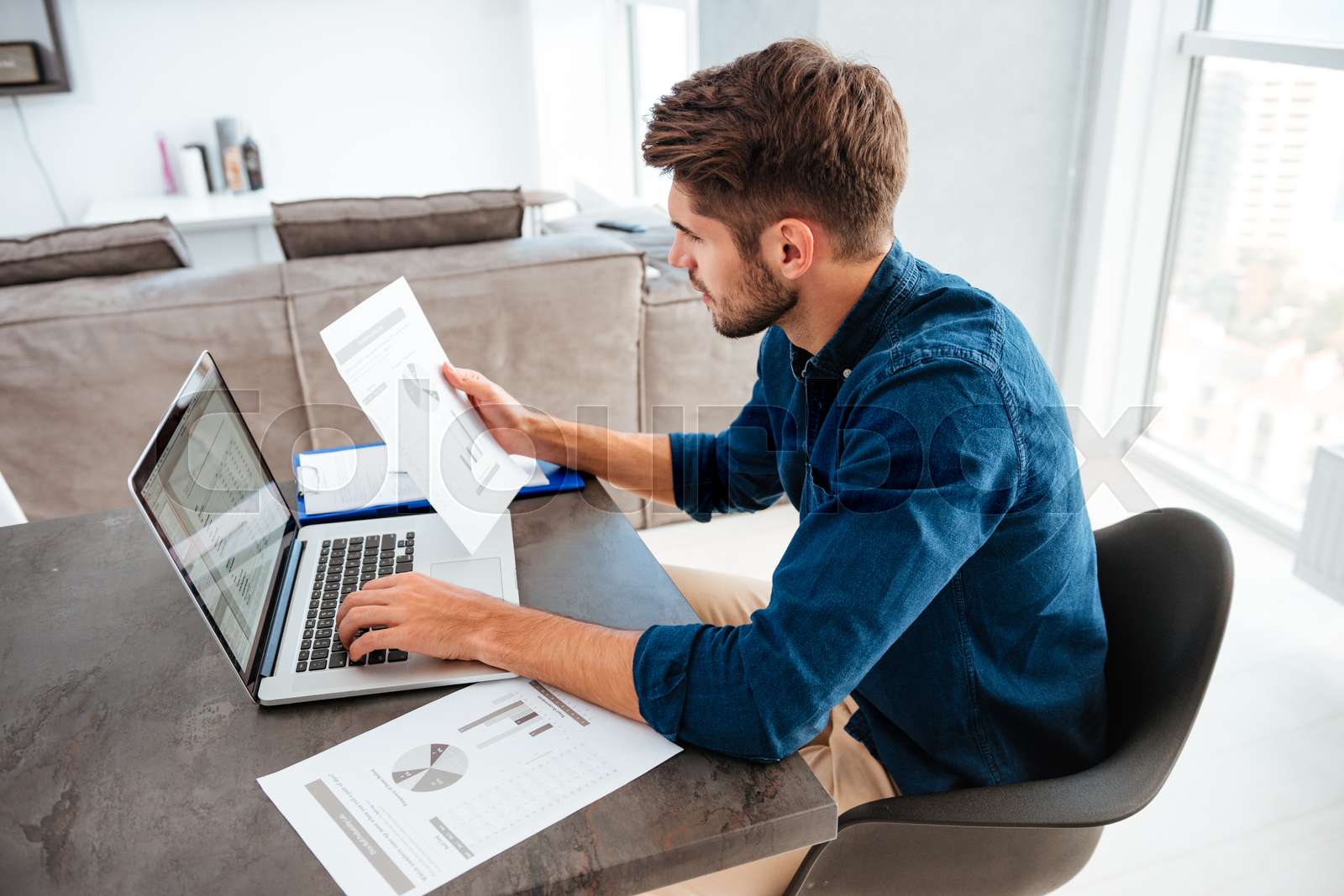 Man using laptop while looking on papers | Stock image | Colourbox