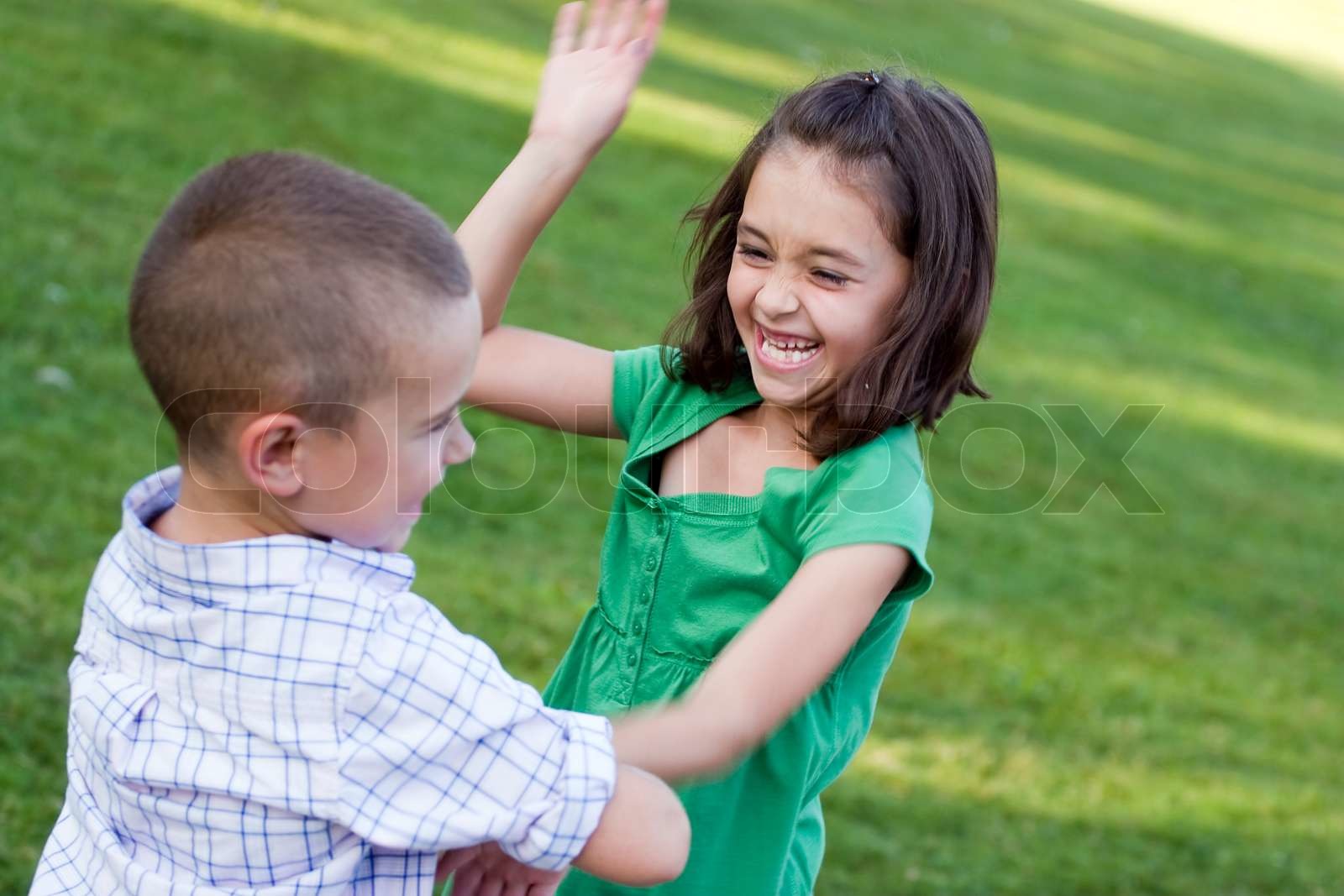 A little girl swings her arms at her brother as they rough house ...