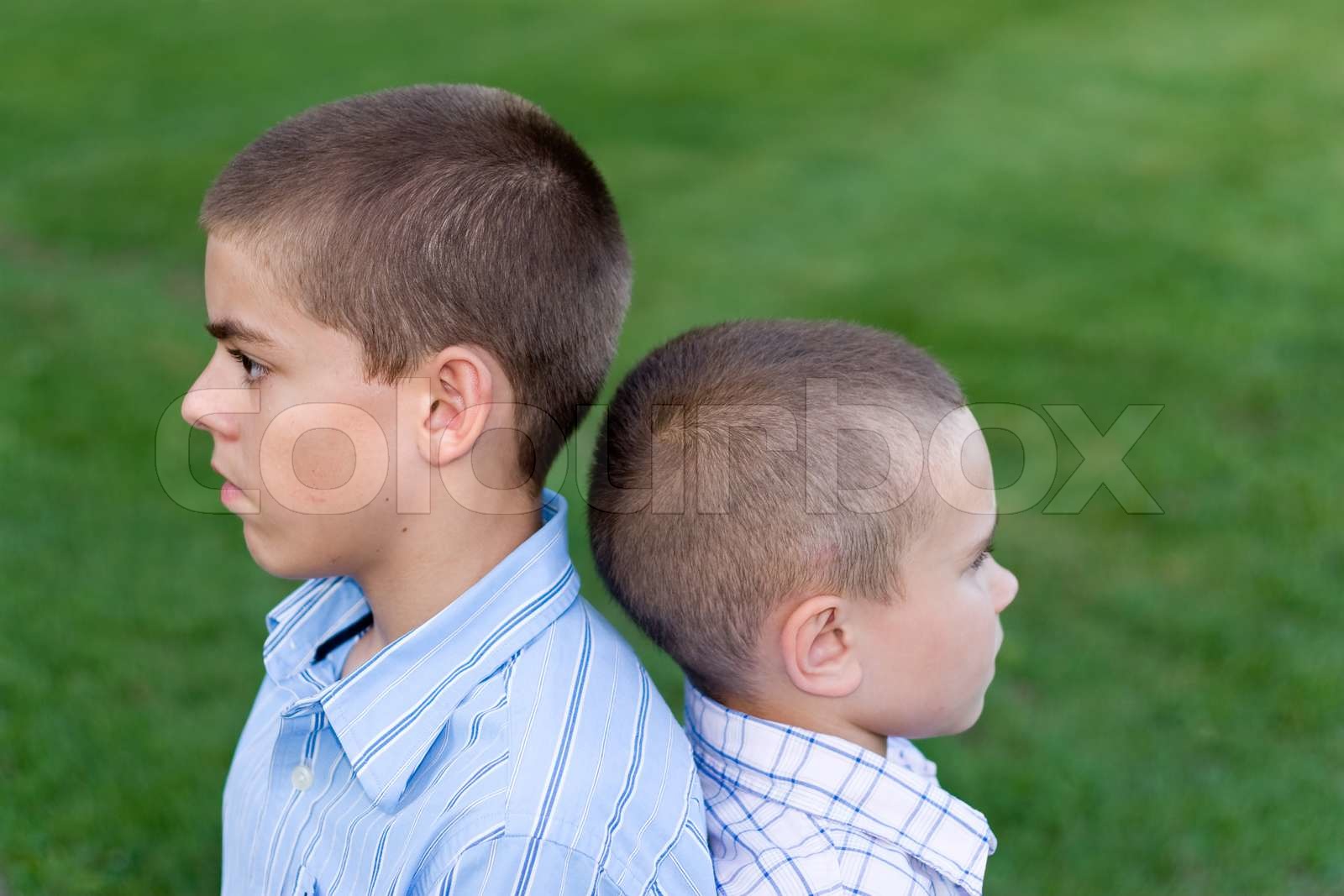 Two young boys sitting back to back outdoors | Stock image | Colourbox