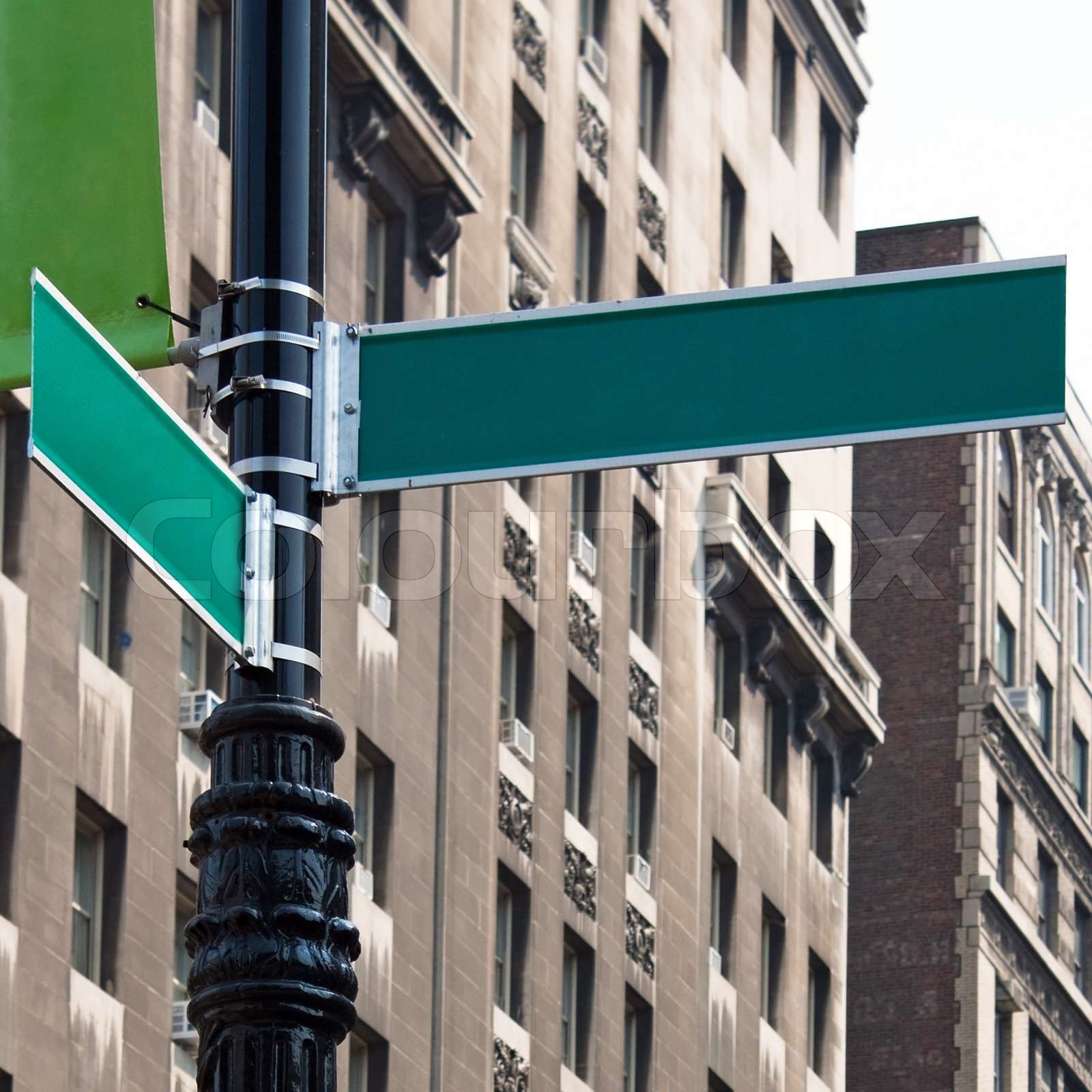 Two blank green street signs on a post at the intersection of two city ...