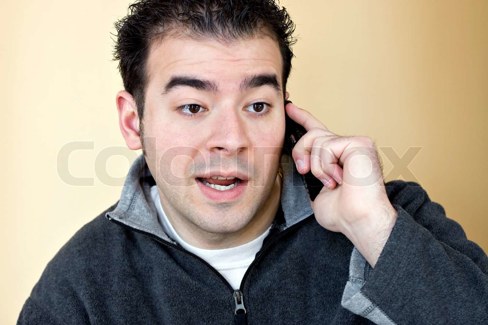 A young man talking on his cell phone with a concerned look on his face ...