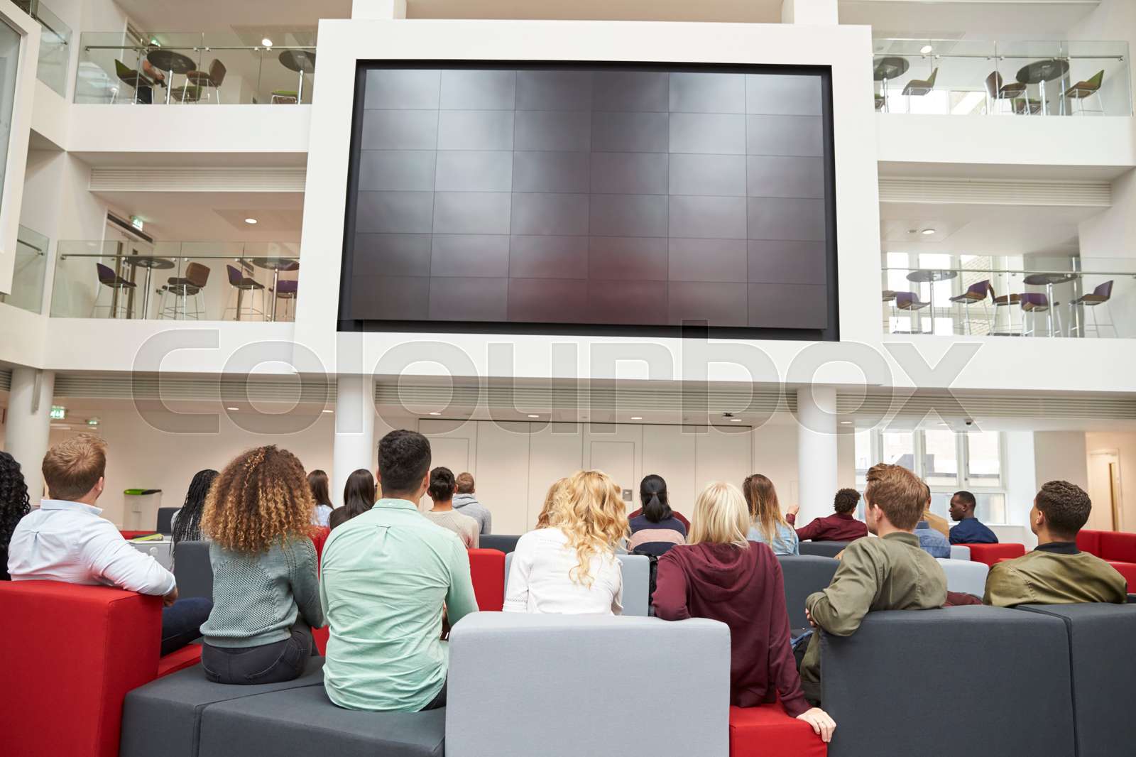 Students watching big screen in university atrium, back view | Stock ...