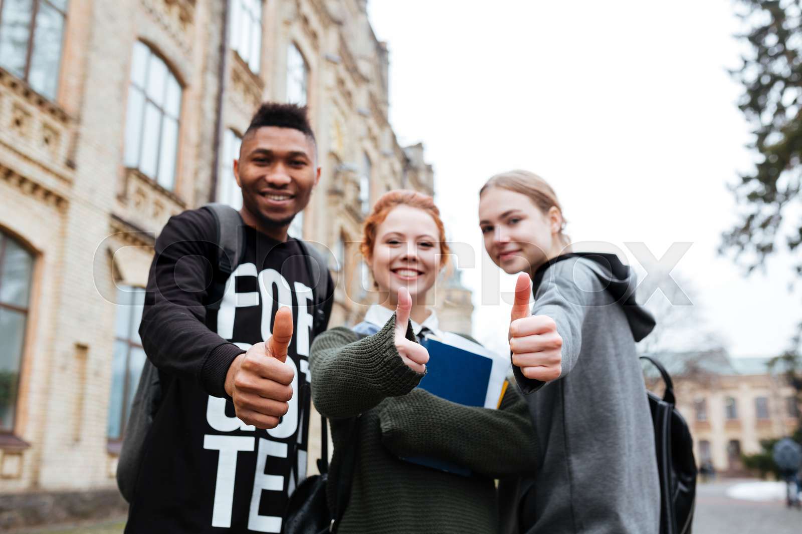 Students standing at the university camous and showing thumbs up ...