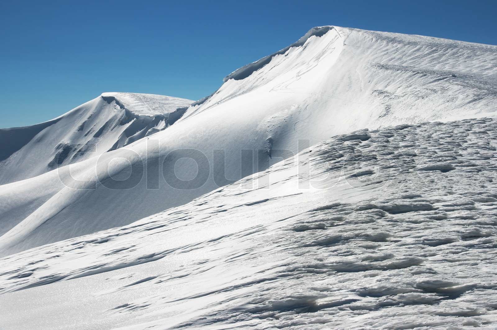 Winter mountains ridge with overhang snow caps and snowboard tracks on ...