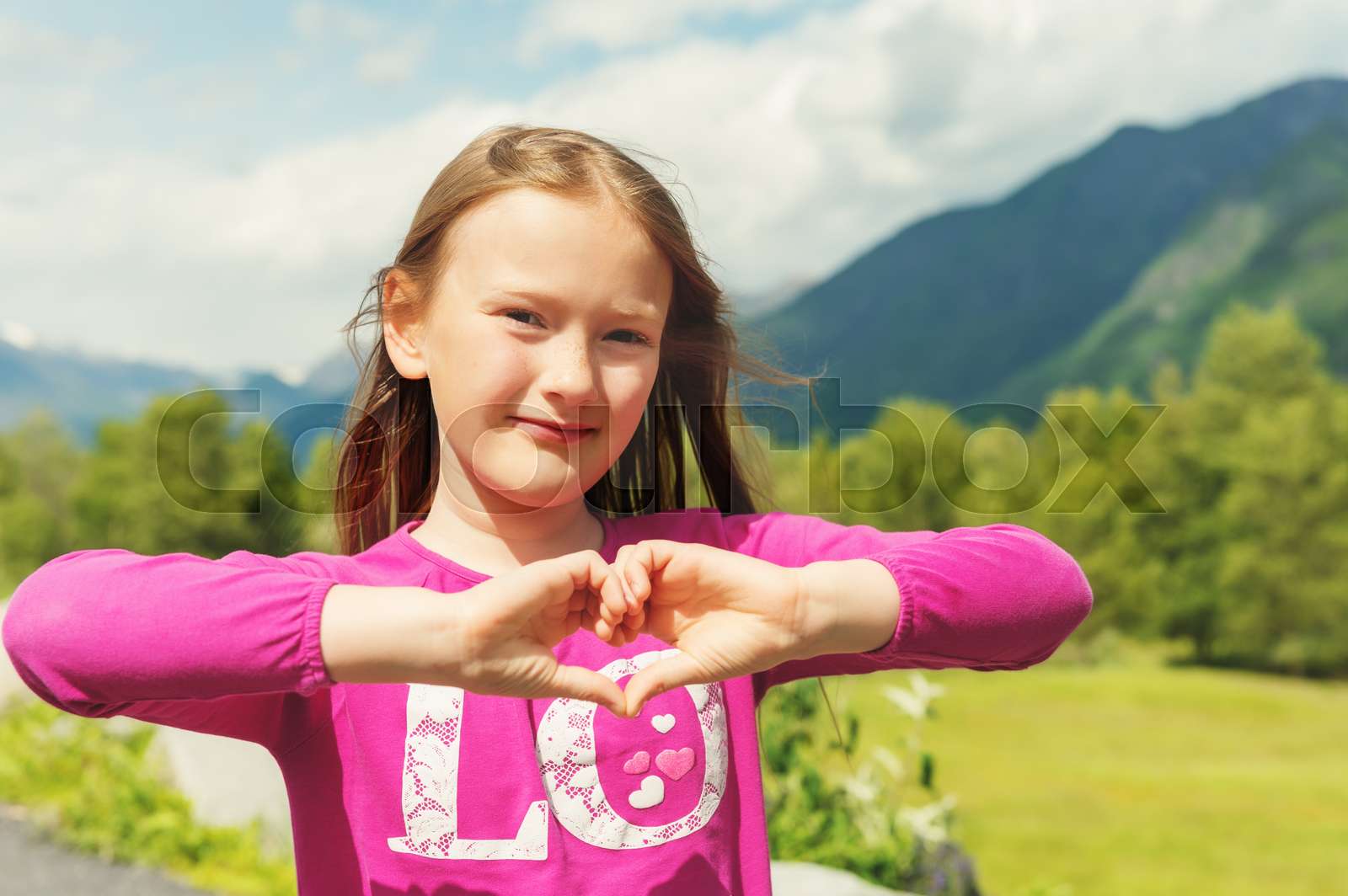 Outdoor portrait of a cute little girl making heart sign with her hands ...