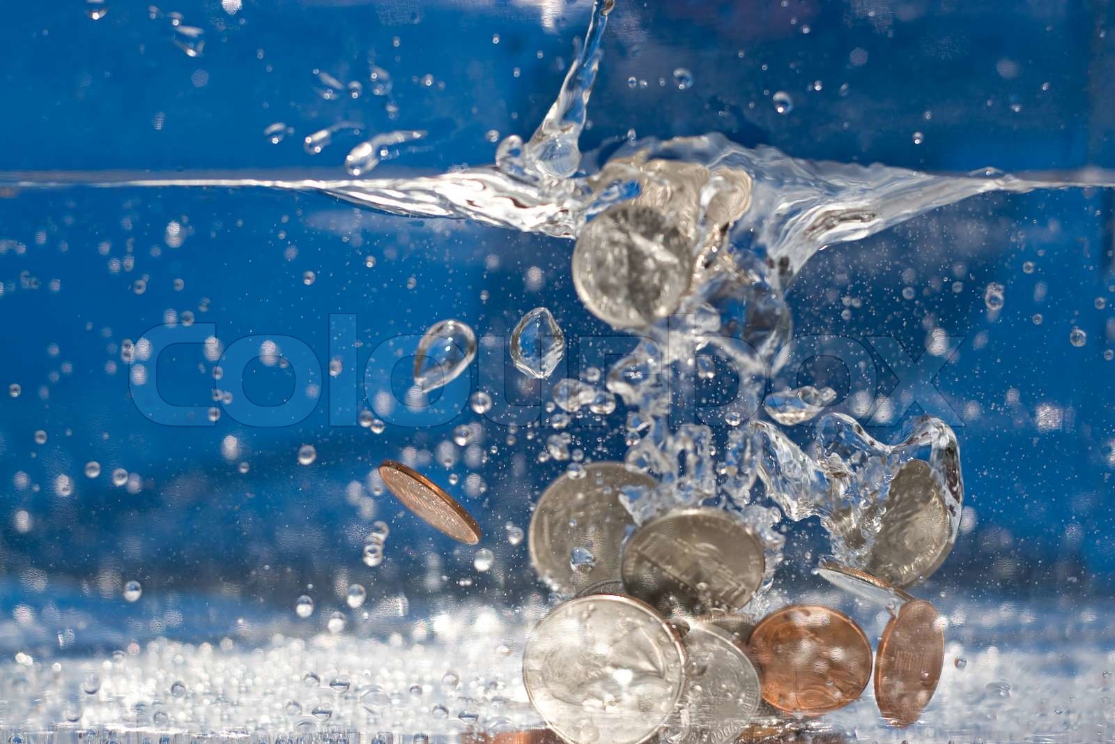 A handful of coins dropping into a pool of water | Stock image | Colourbox
