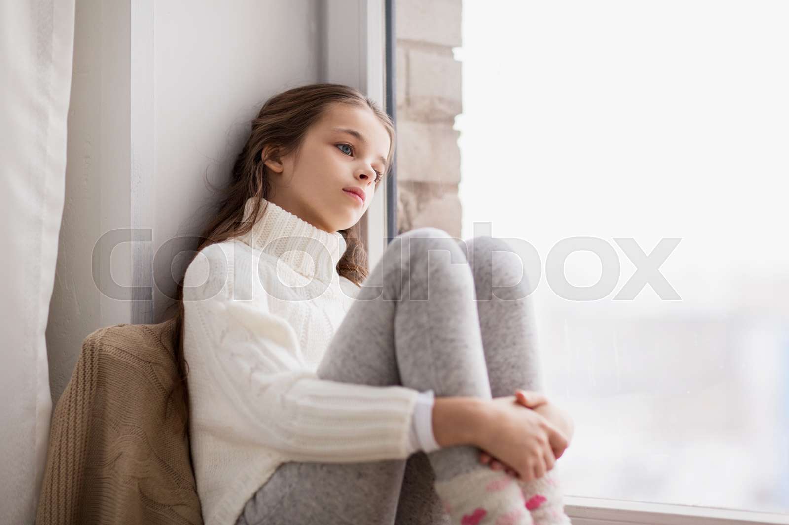sad girl sitting on sill at home window in winter | Stock image | Colourbox