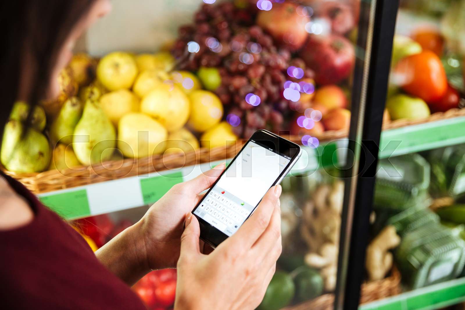 Woman using cell phone in grocery store | Stock image | Colourbox