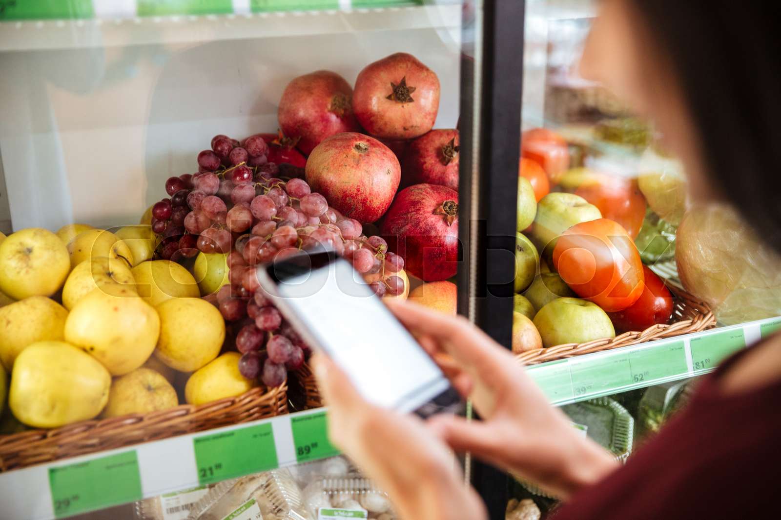 Woman choosing fruits and using cell phone in grocery shop | Stock ...