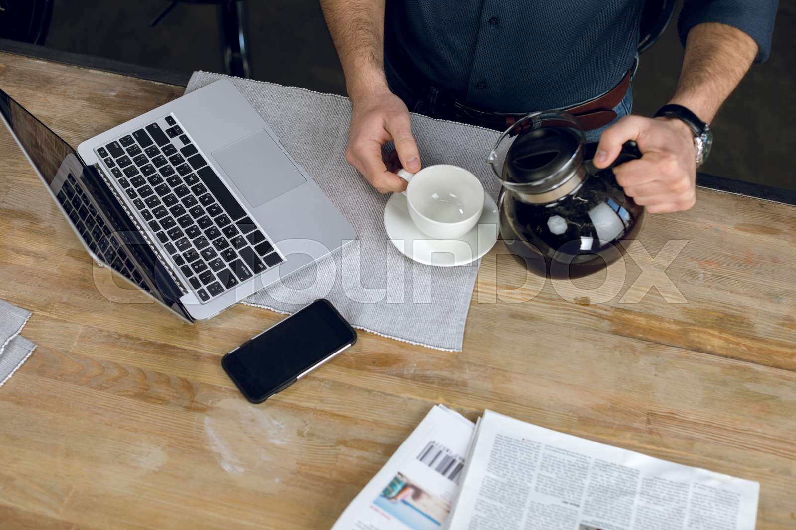 man pouring coffee in cup on desk with laptop and newspapers | Stock ...