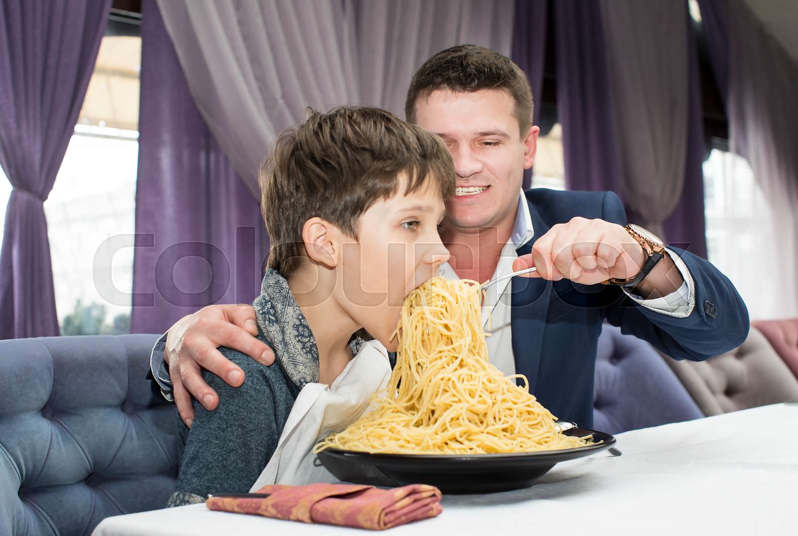 Dad feeding his son spaghetti in a restaurant | Stock image | Colourbox