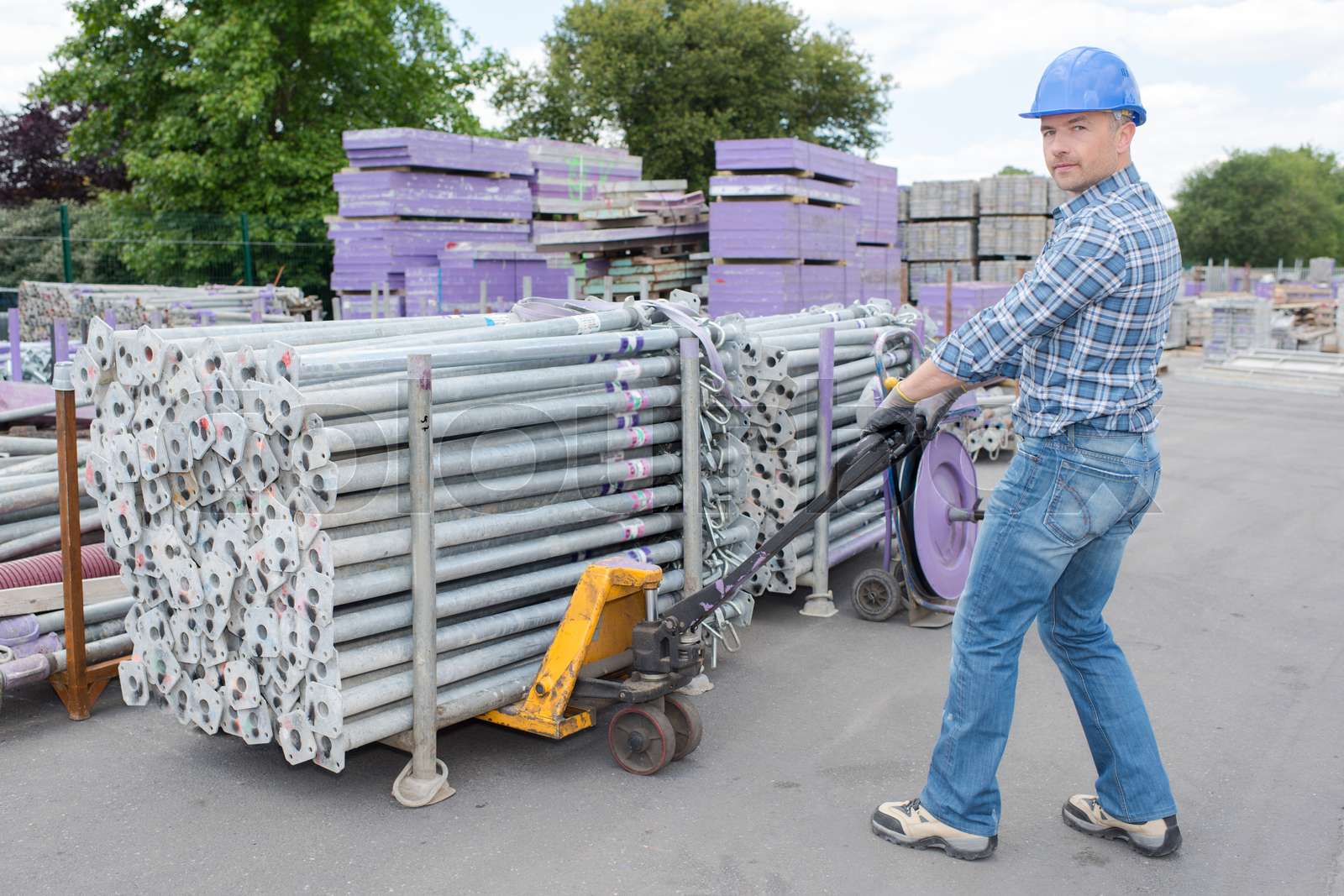 Worker moving pallet of scaffold poles | Stock image | Colourbox