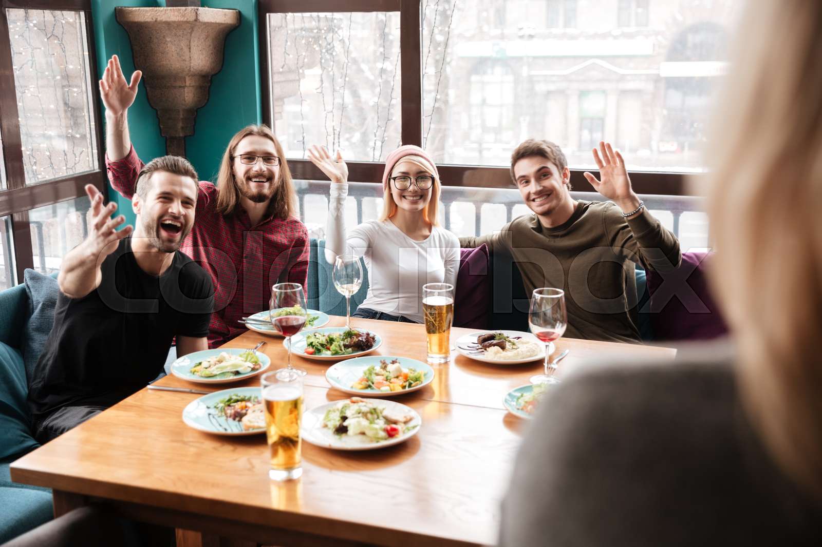 Happy friends sitting in cafe while waving | Stock image | Colourbox