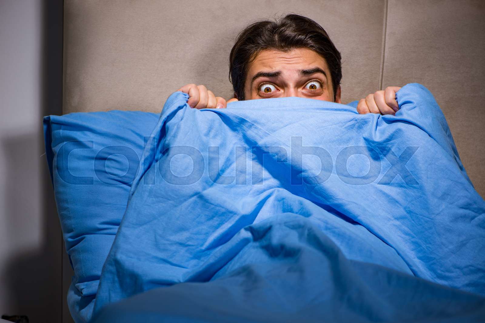 Young man scared in bed | Stock image | Colourbox