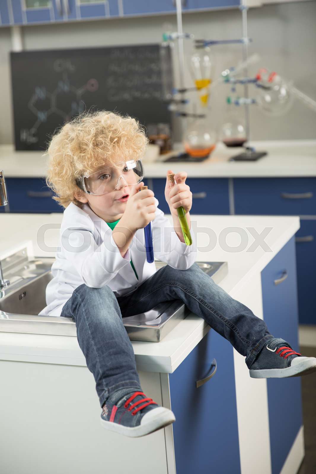 Little boy sitting in sink in science laboratory and holding test tubes ...