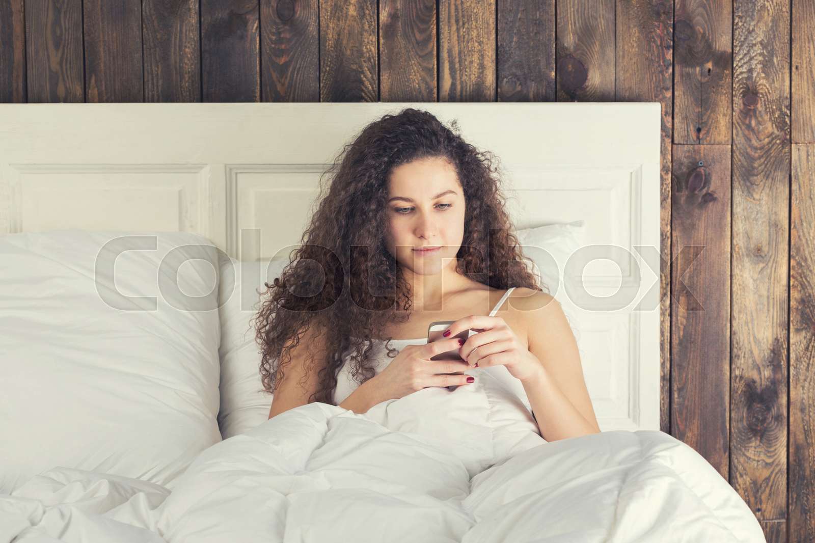 Beautiful girl watching in the phone lie in bed | Stock image | Colourbox