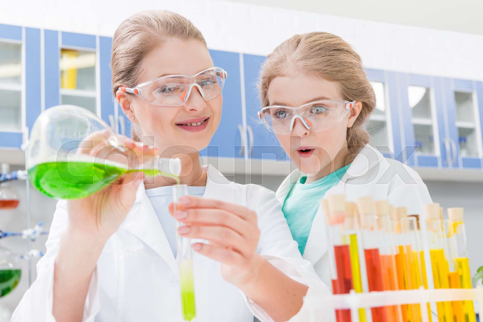 adult scientist and excited girl in goggles mixing reagents in tubes in ...