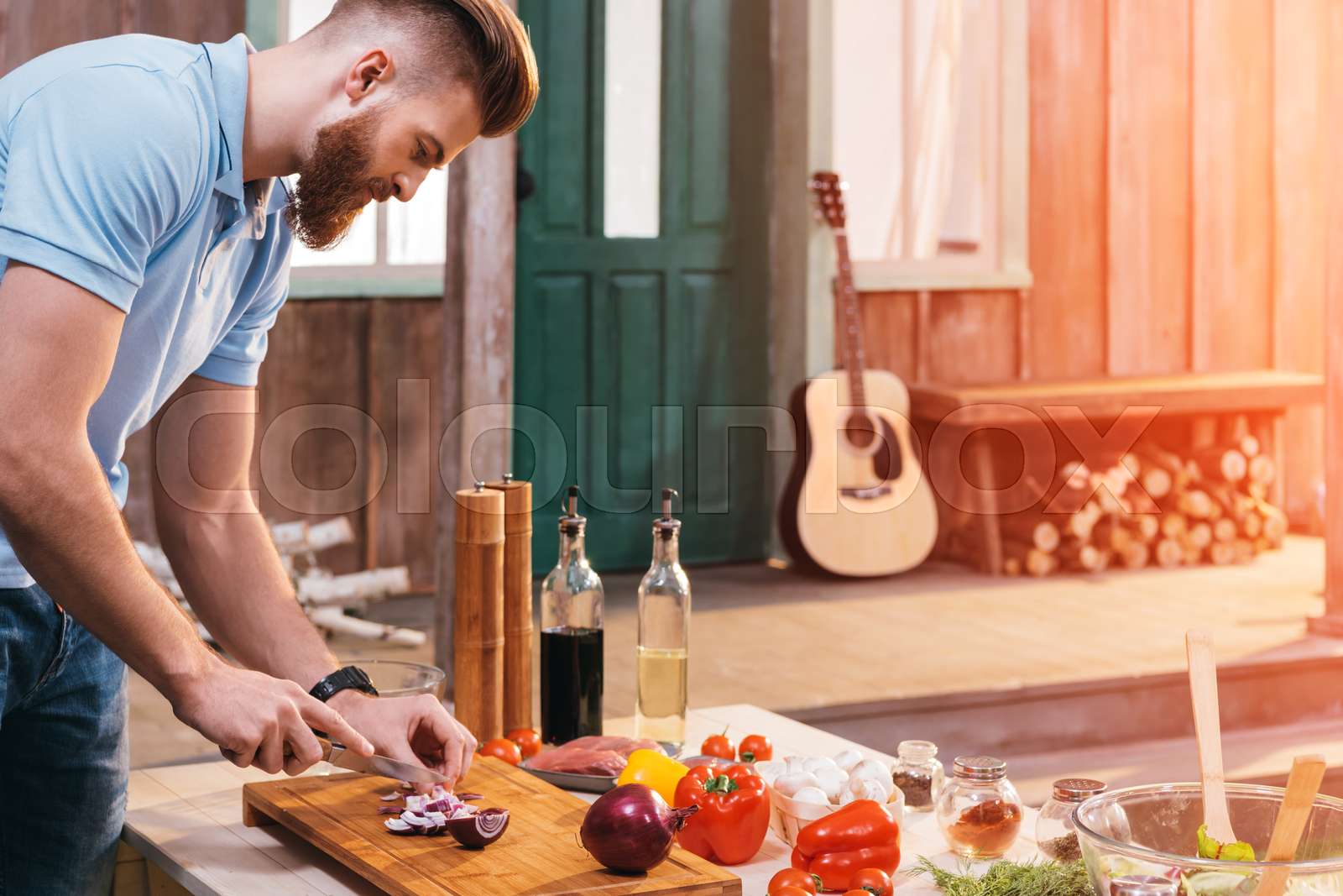 Side view of bearded young man cutting onion for barbecue | Stock image ...