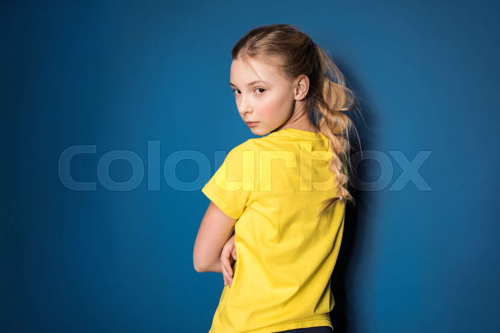 rear view of preteen girl in yellow shirt in studio isolated on blue ...