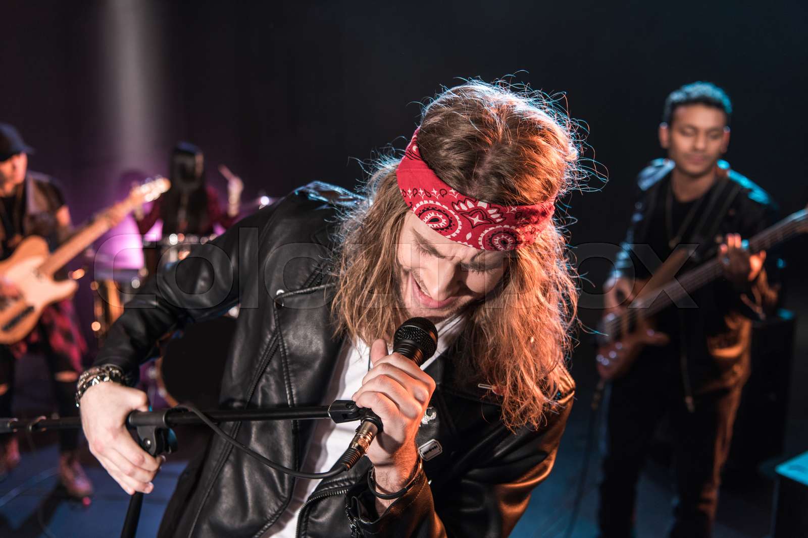 Handsome singer with rock and roll band performing music on stage ...