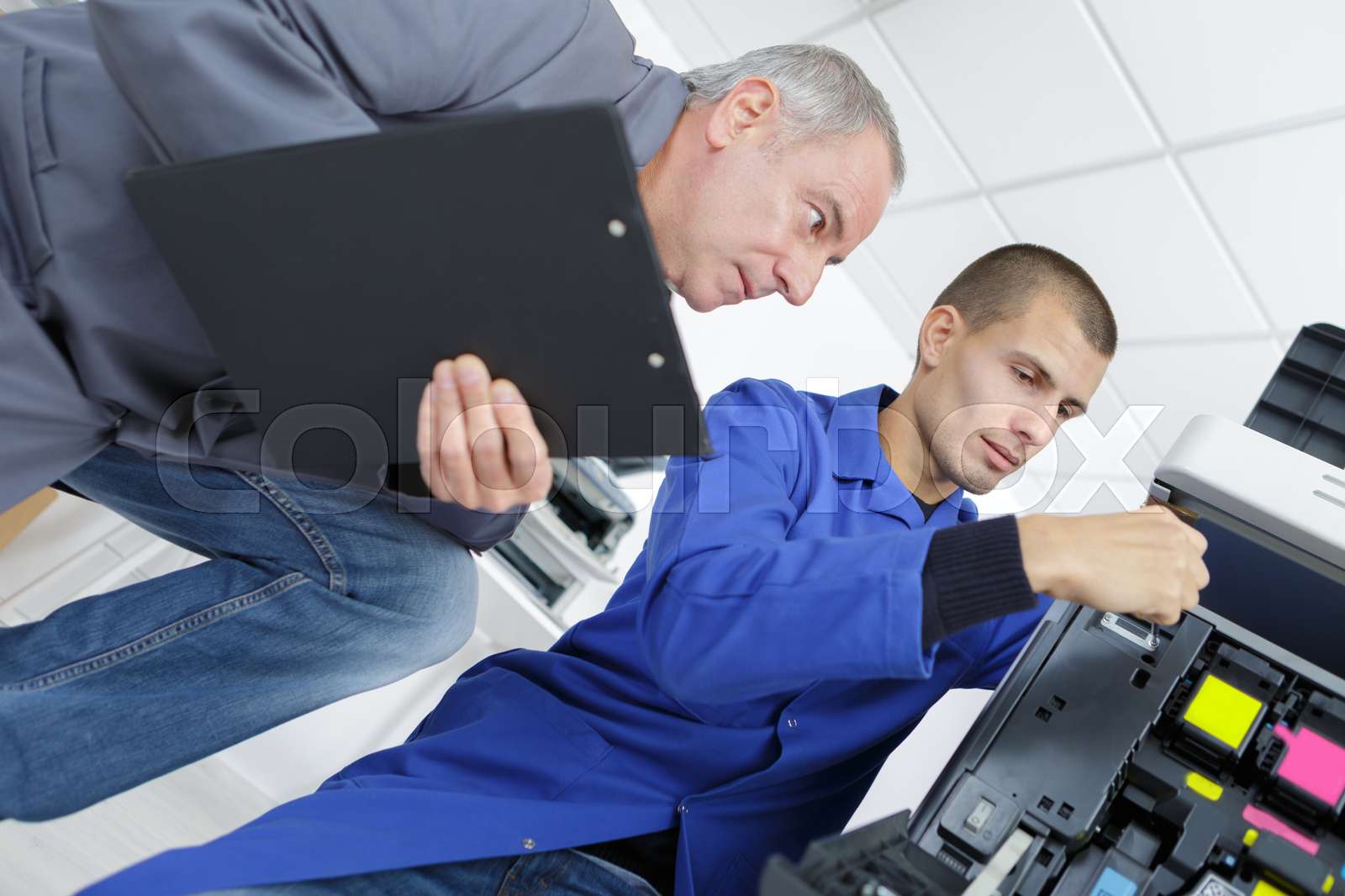 Supervisor watching technician work on photocopier | Stock image ...