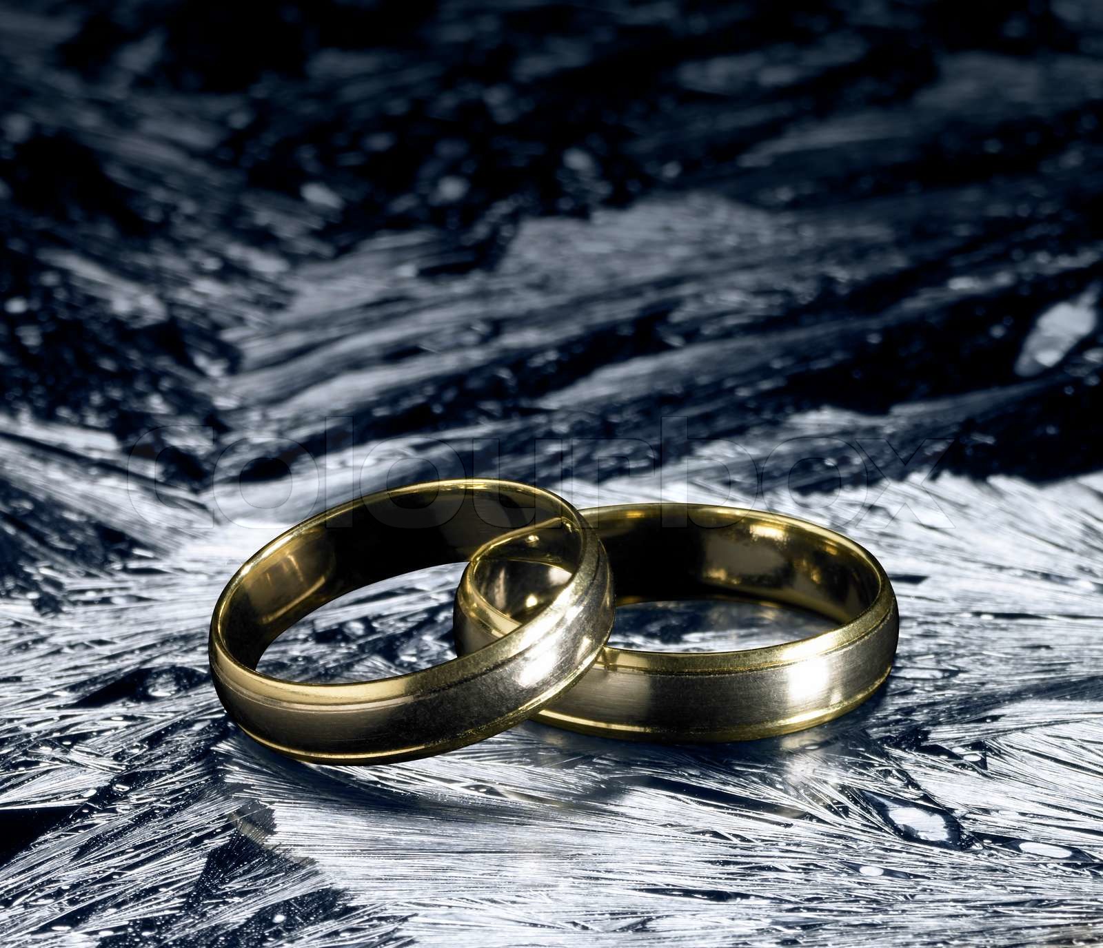 studio photography of two golden wedding rings on each other in icy ...