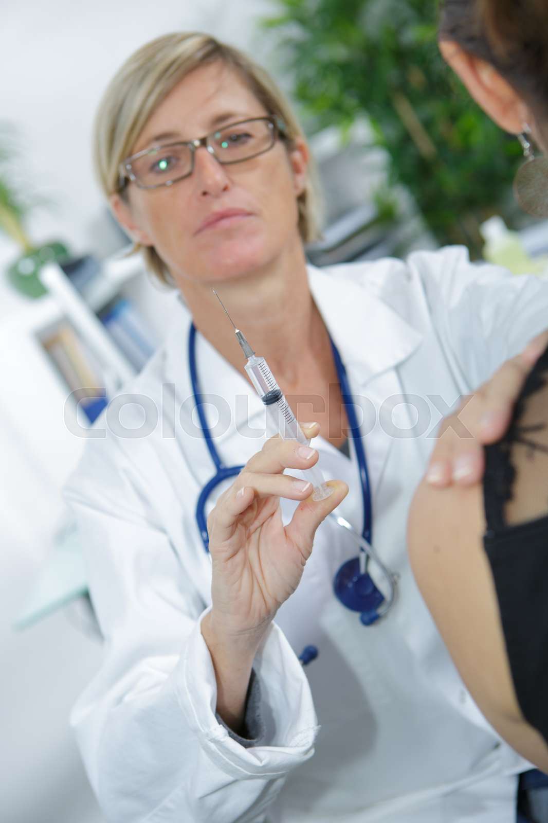 Nurse preparing injection for woman's arm | Stock image | Colourbox