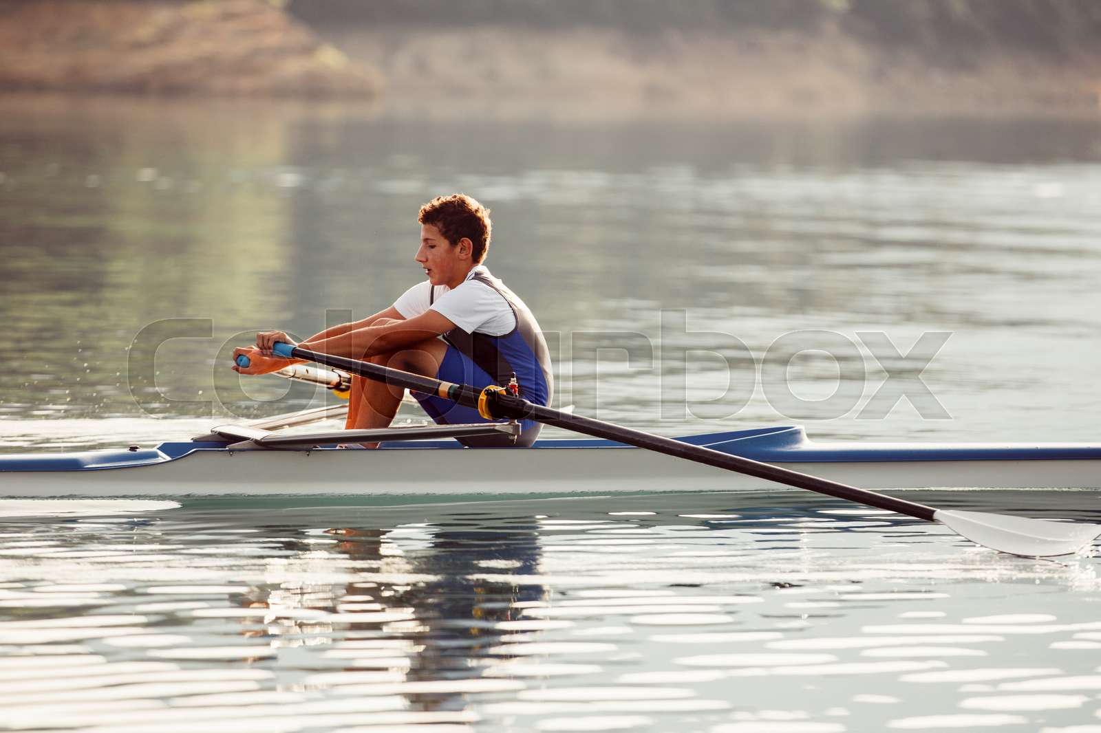 A Young single scull rowing competitor paddles on the tranquil lake ...