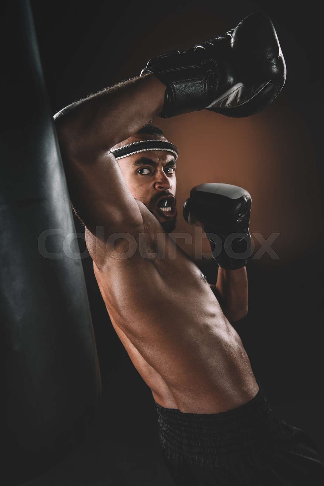 Aggressive young Muay Thai fighter in boxing gloves training thai ...