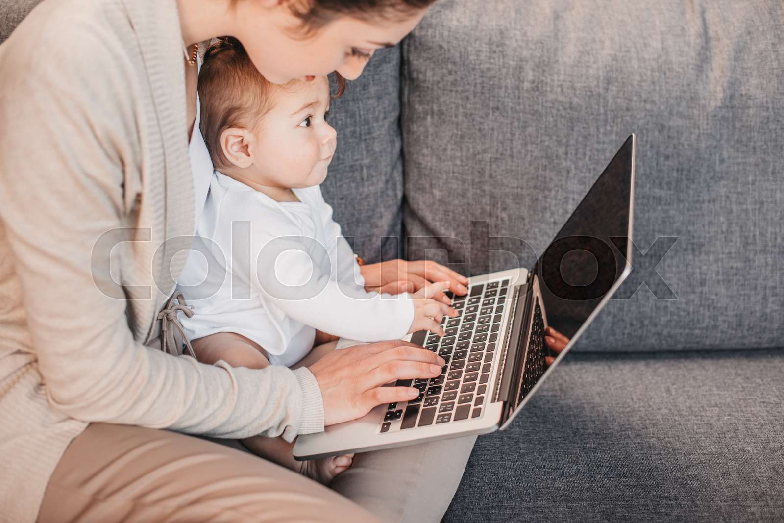 Side view of young mother typing on laptop's keyboard with her son ...