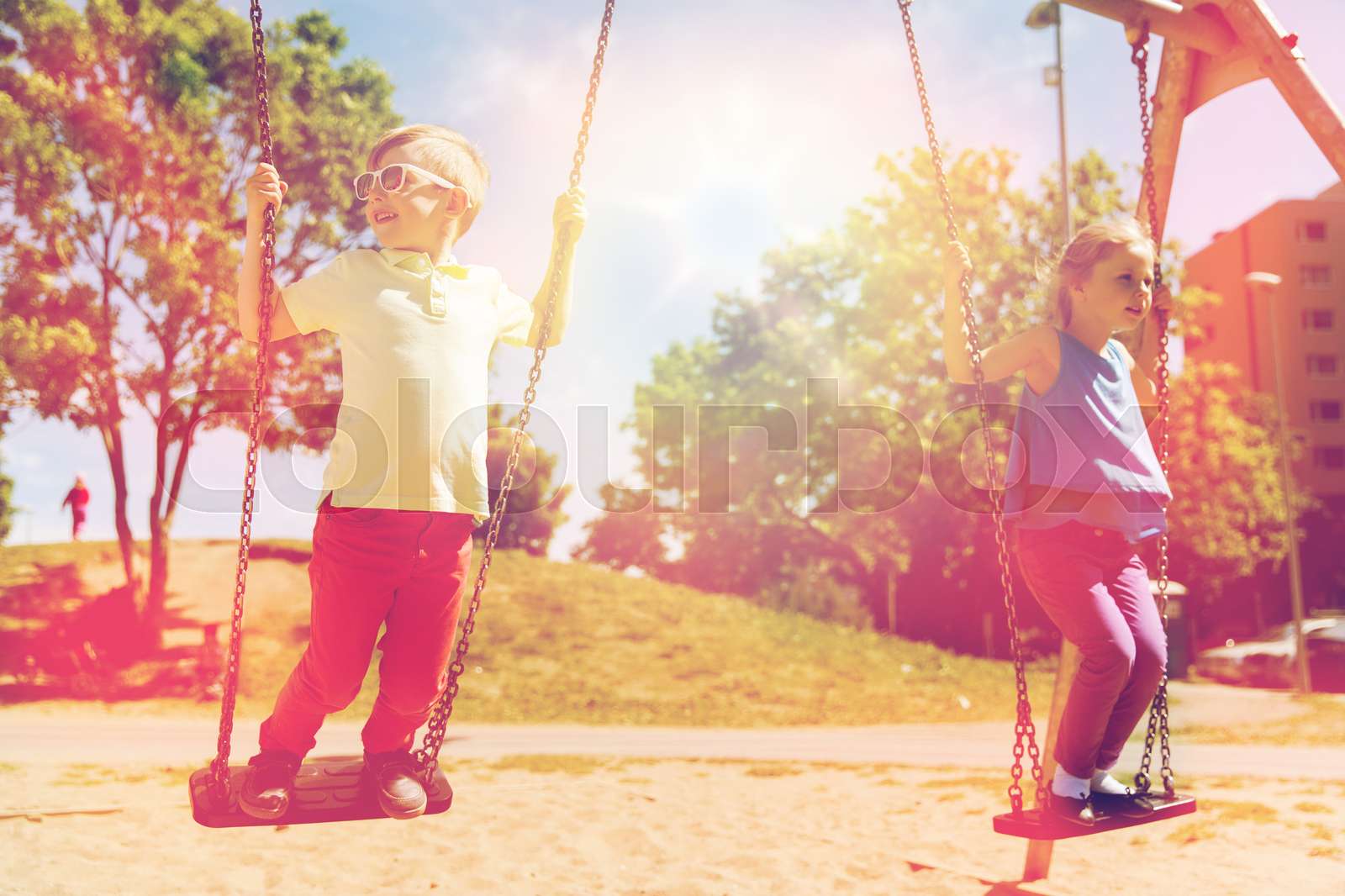 two happy kids swinging on swing at playground | Stock image | Colourbox