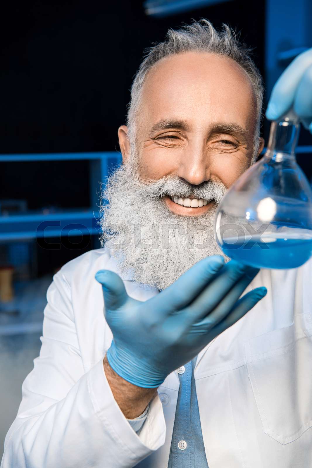 happy grey haired scientist in lab coat holding flask with reagent at ...