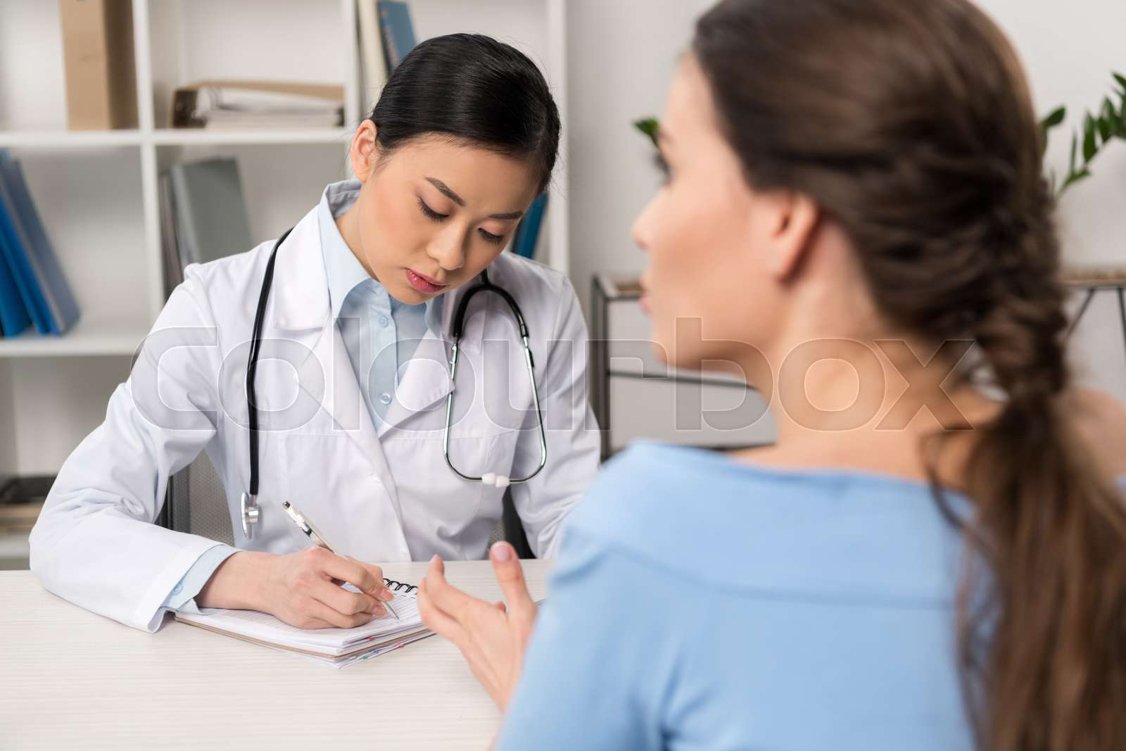 doctor writing in notebook while patient telling about illness at ...