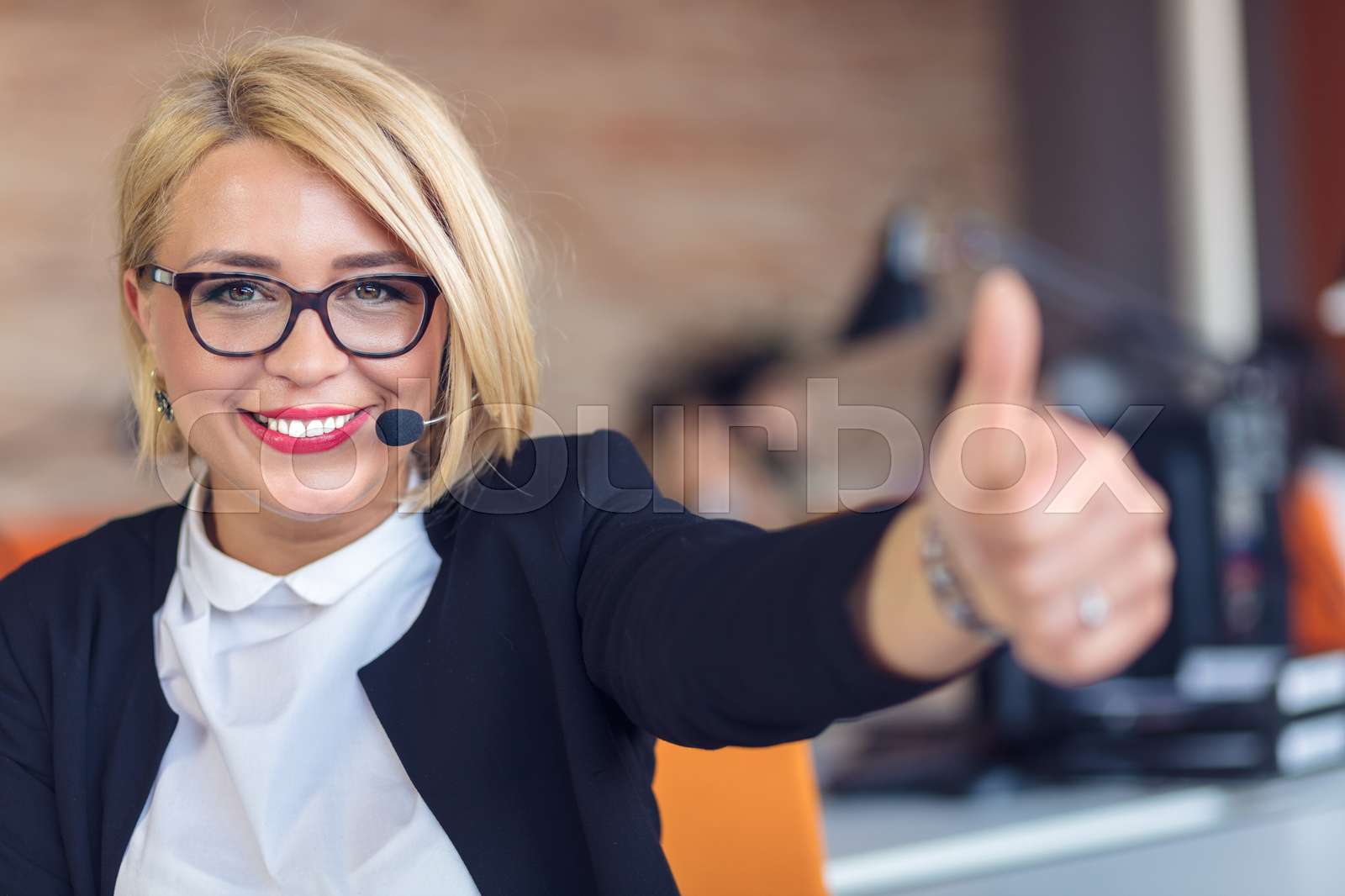Young woman sitting behind desk with thumbs up in an office | Stock ...