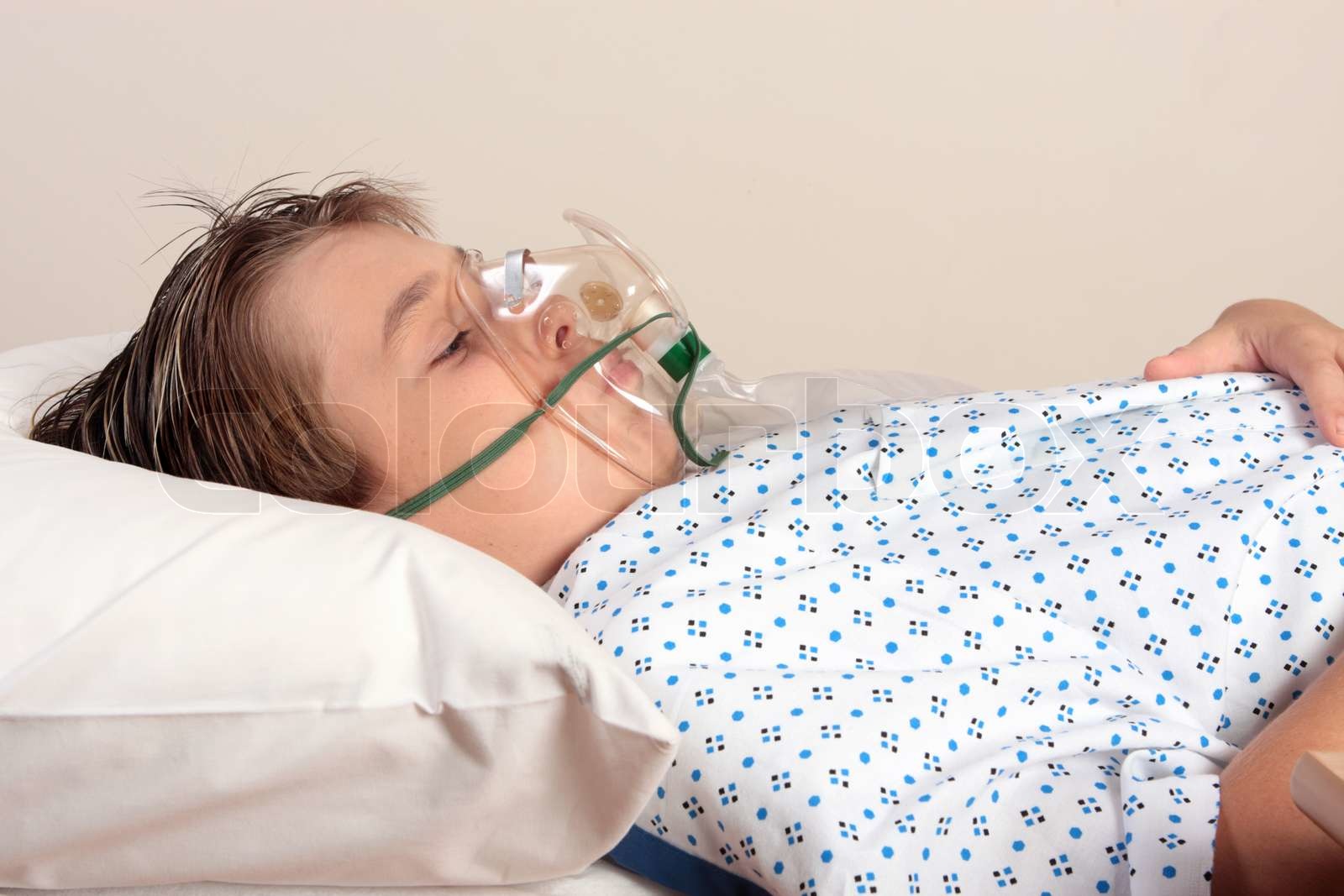A child resting on a bed wearing patient gown has an oxygen mask or ...