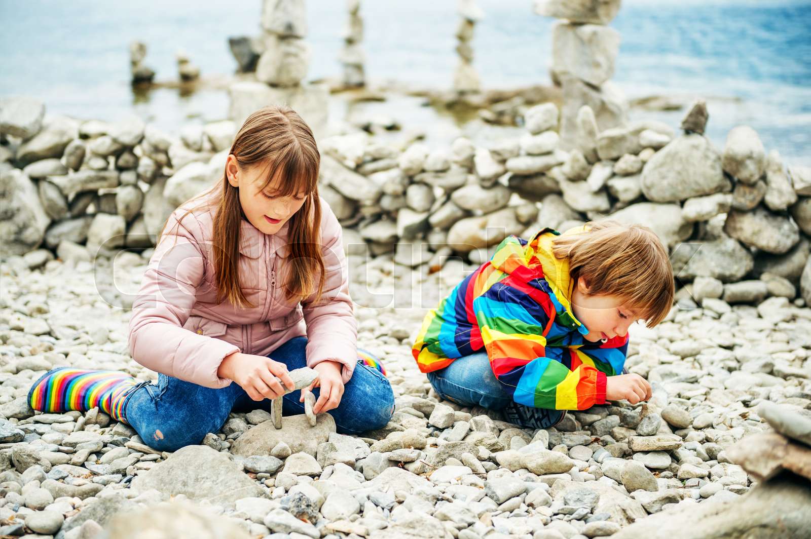 Kids playing between stacks of stones on the beach | Stock image ...