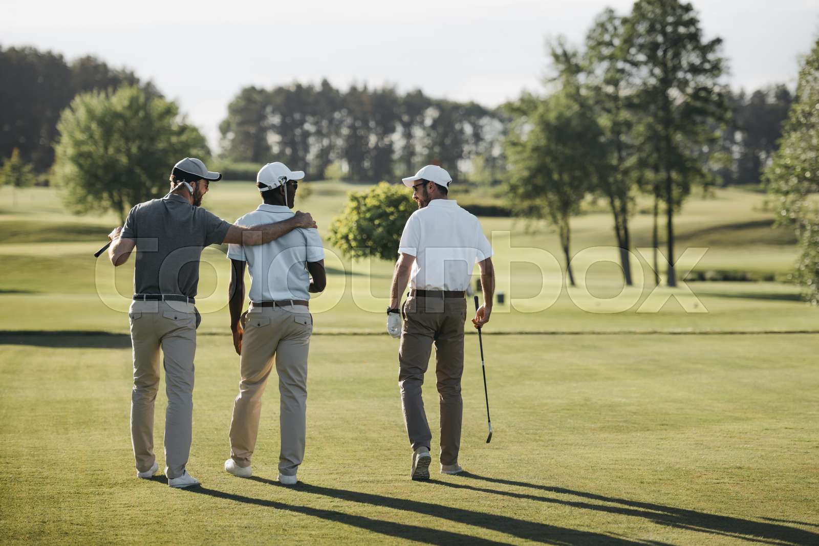 back view of multiethnic golf players hugging and walking on golf ...