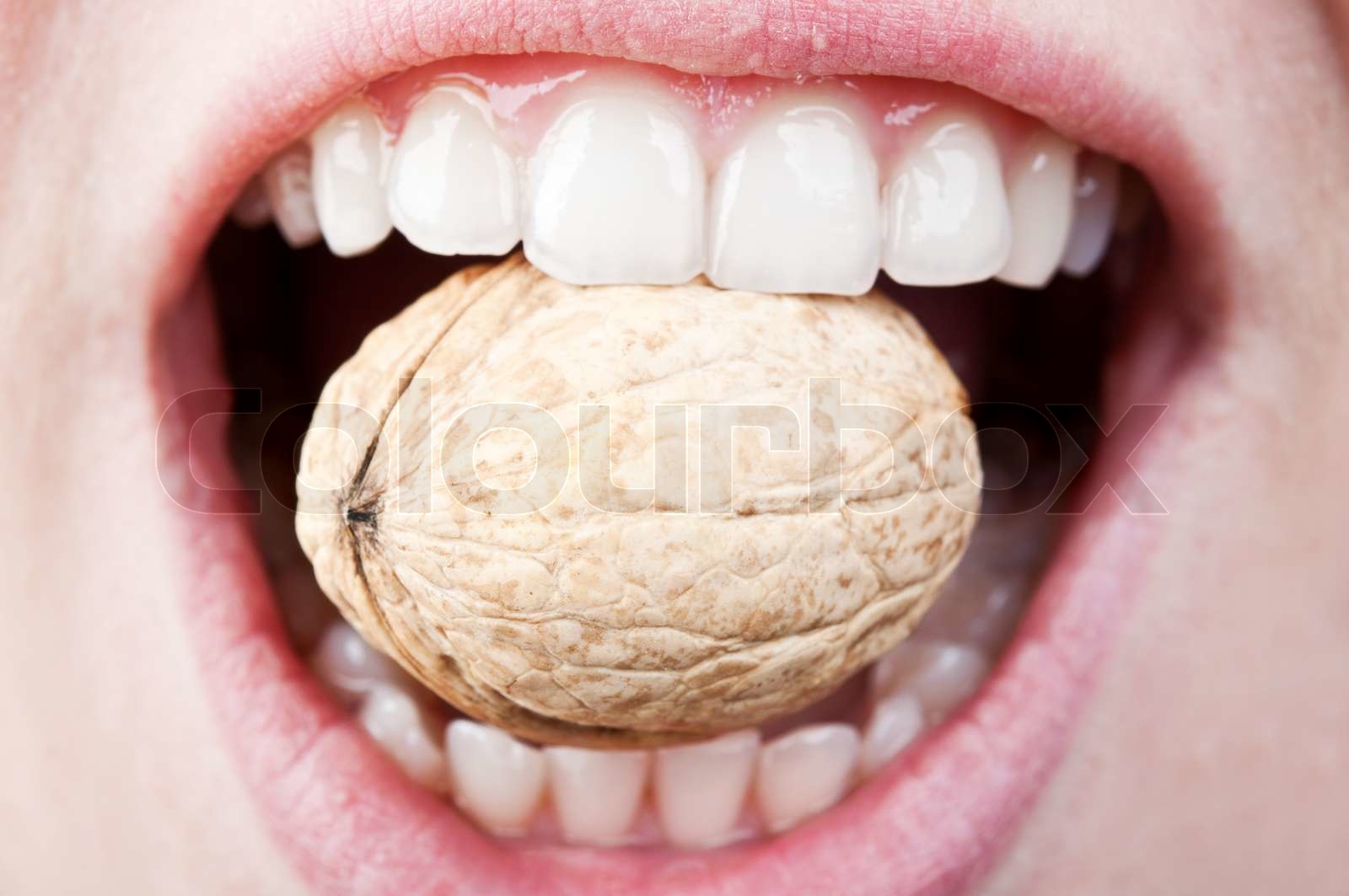 a woman with a healthy and beautiful teeth eating hard nut | Stock ...