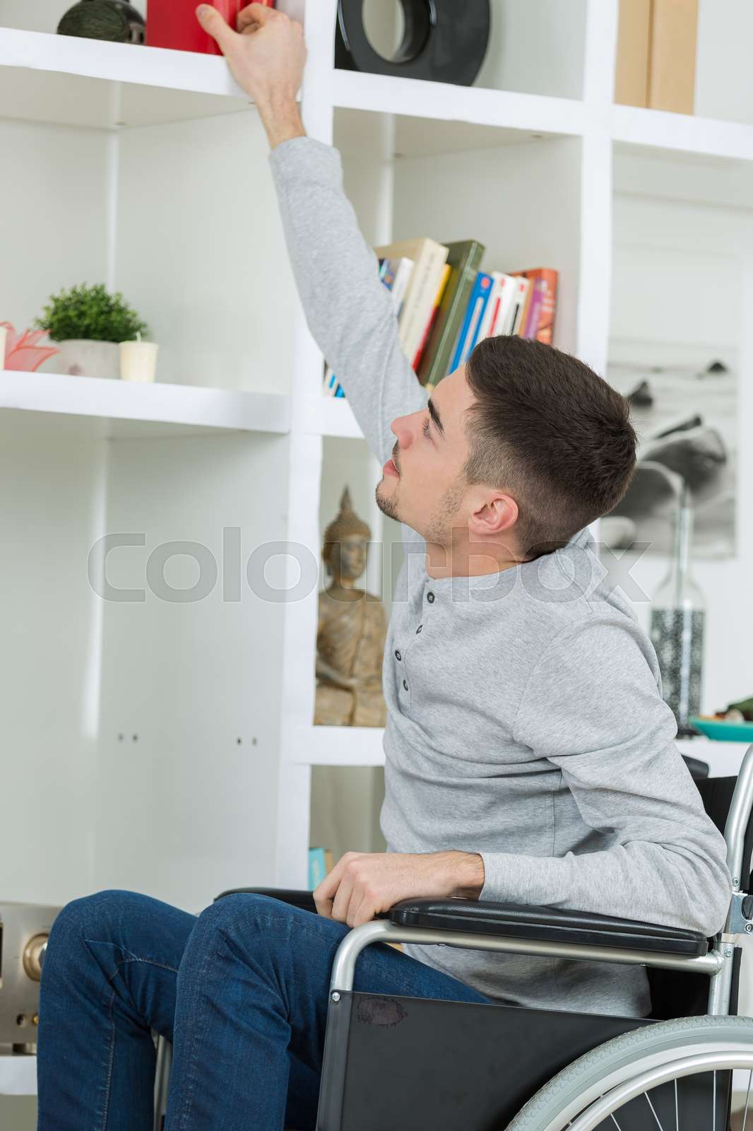Young man in wheelchair reaching for object from high shelf | Stock ...
