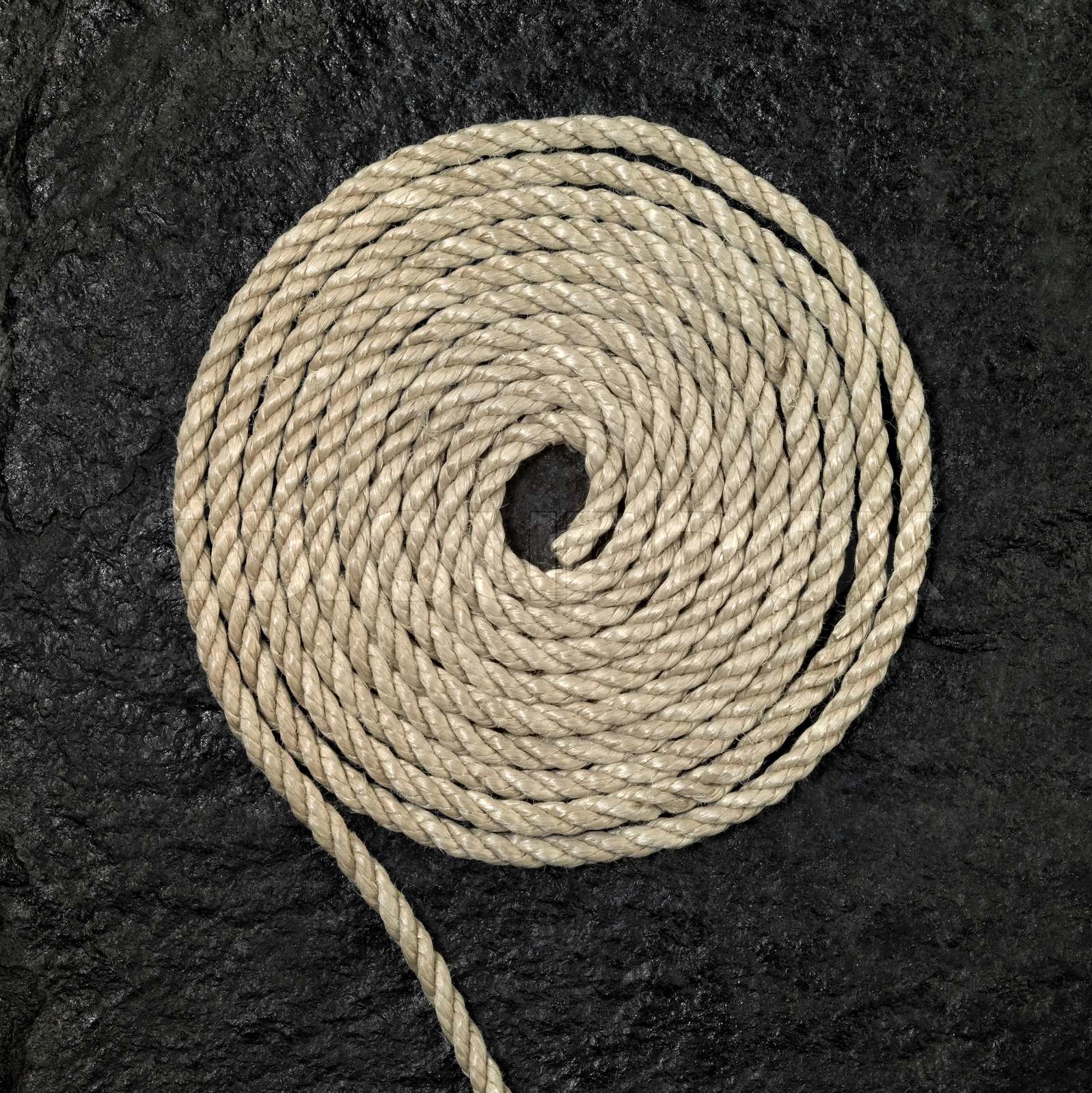 a rolled hemp rope on dark rough stone surface | Stock image | Colourbox