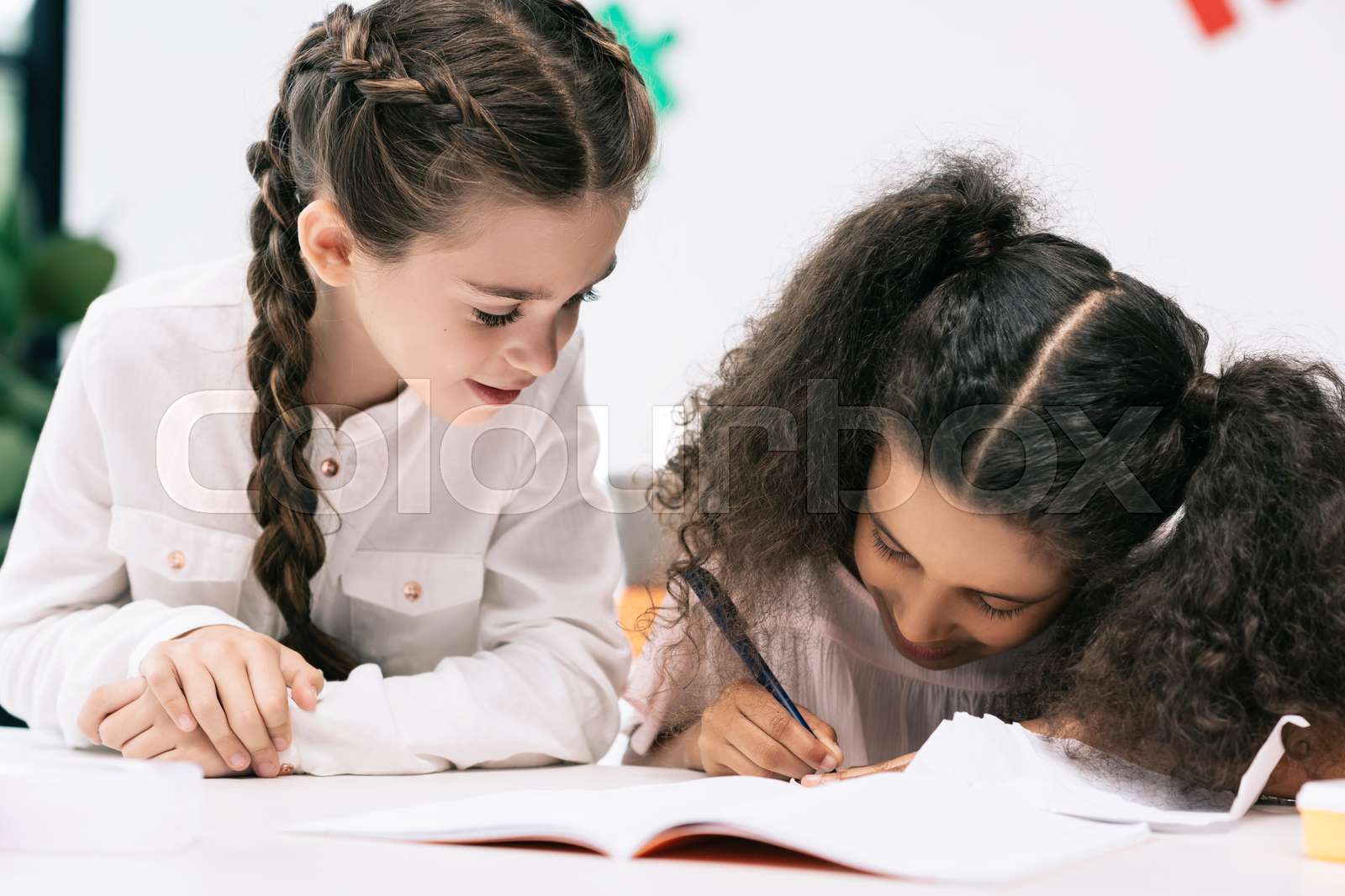 Cute smiling multiethnic schoolgirls studying together in classroom ...