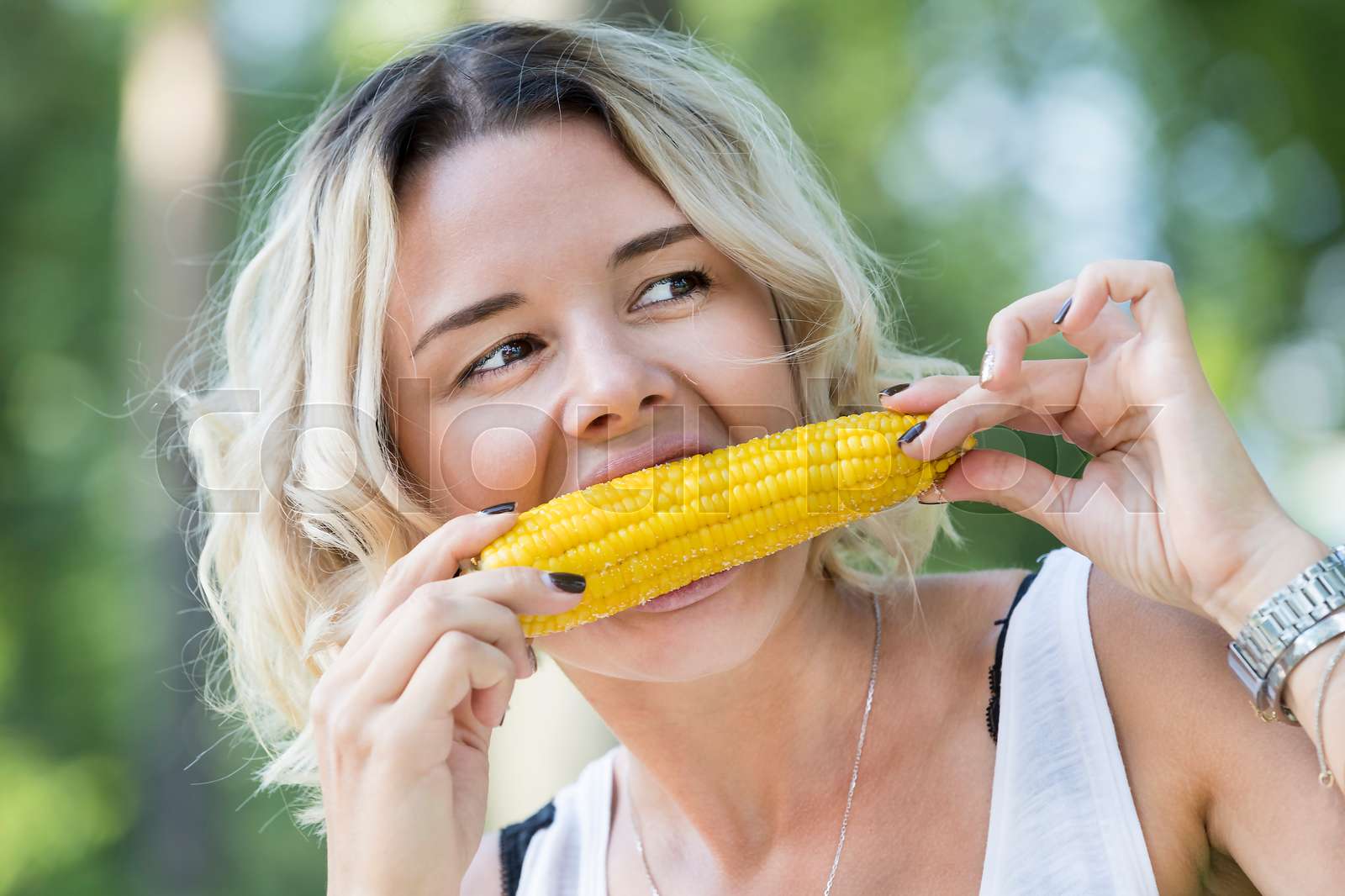 The girl is eating boiled sweet corn in the park | Stock image | Colourbox