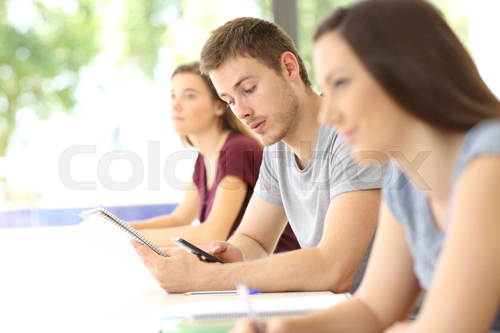 Student distracted with a phone during a class | Stock image | Colourbox