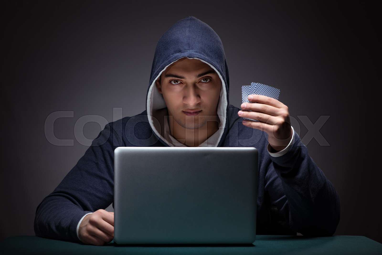 Young man wearing a hoodie sitting in front of a laptop computer ...