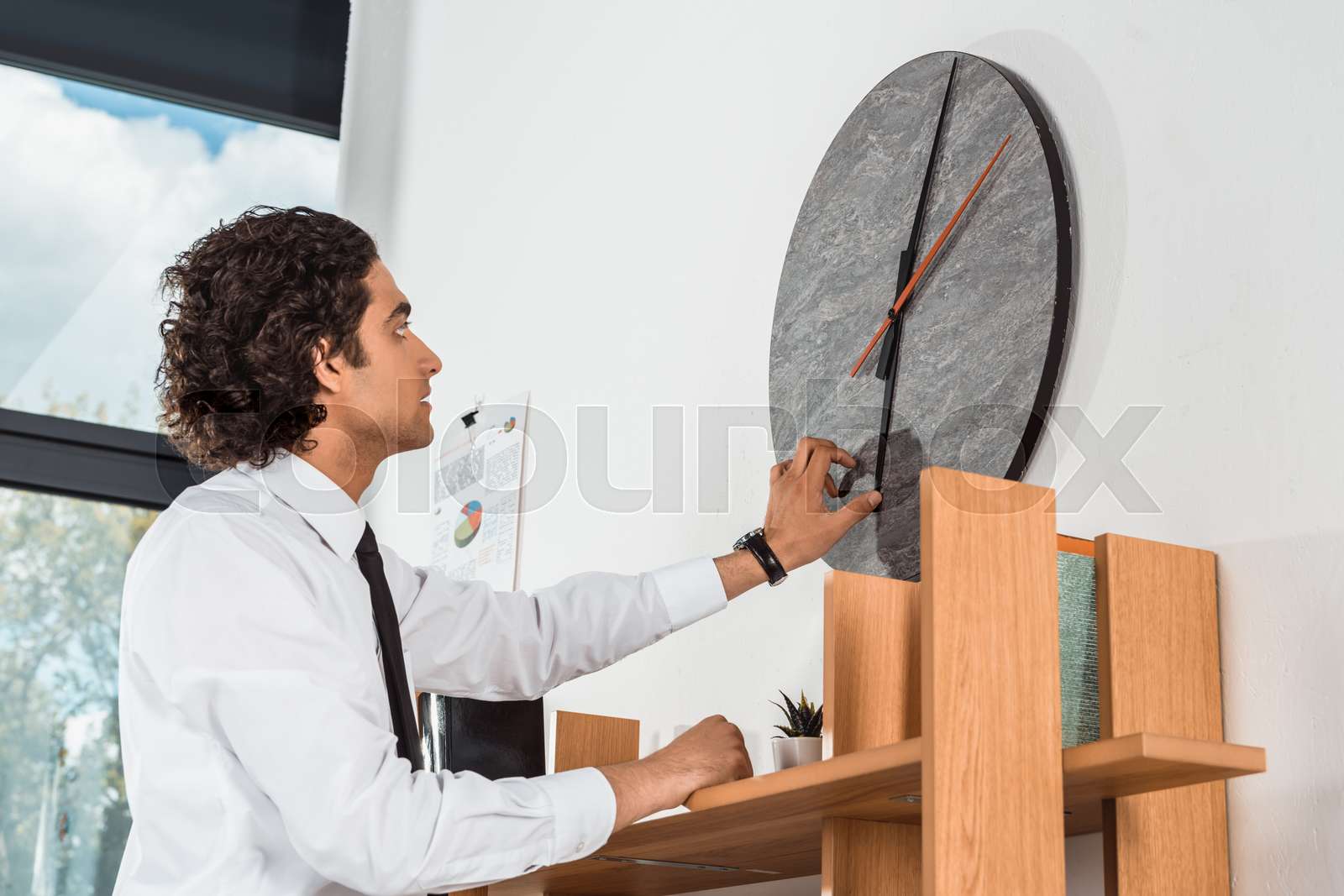 side view of young businessman setting time on clock in office | Stock ...